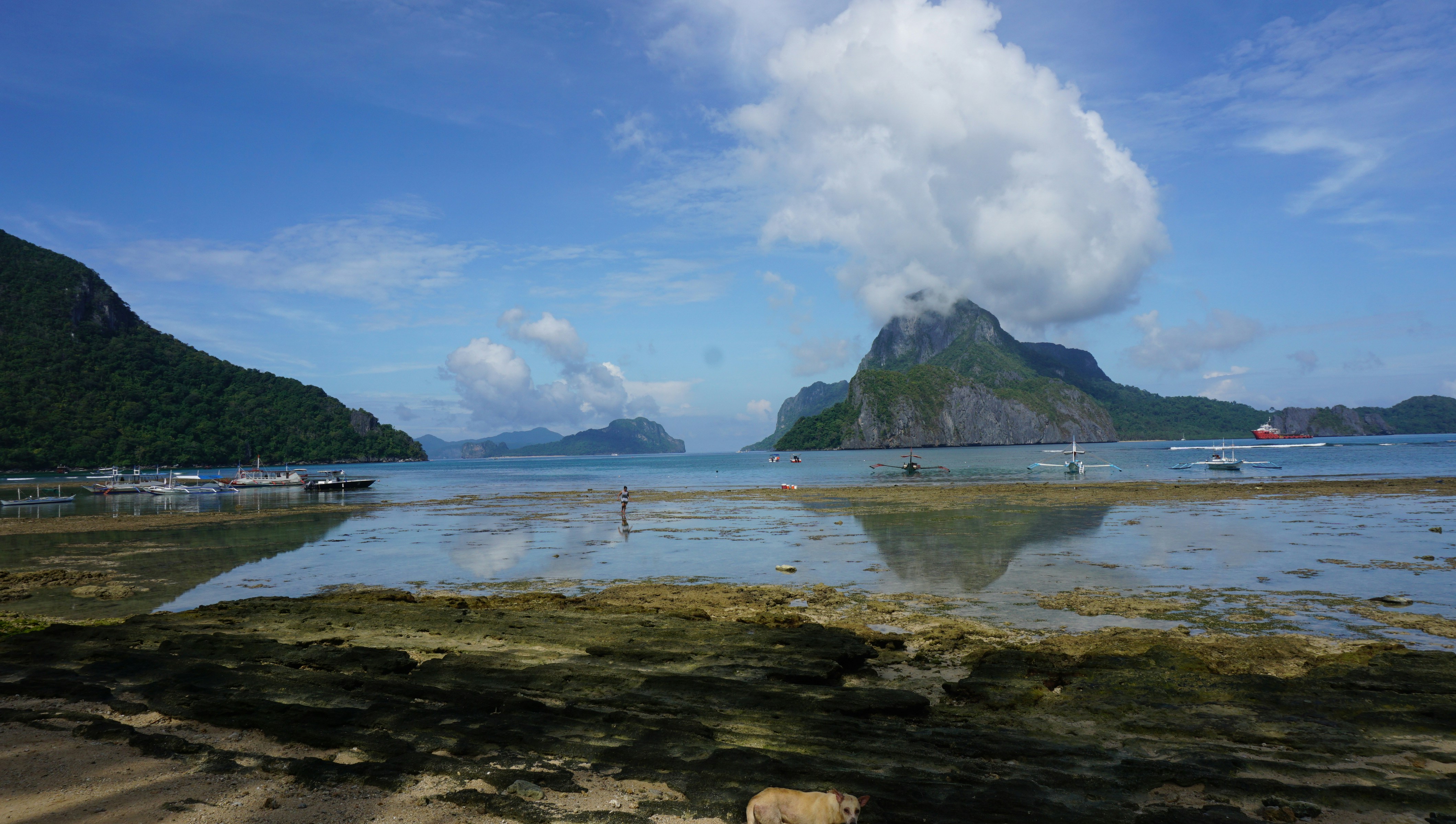 Cloud hovering above a lush island with boats on calm waters near El Nido, Palawan.