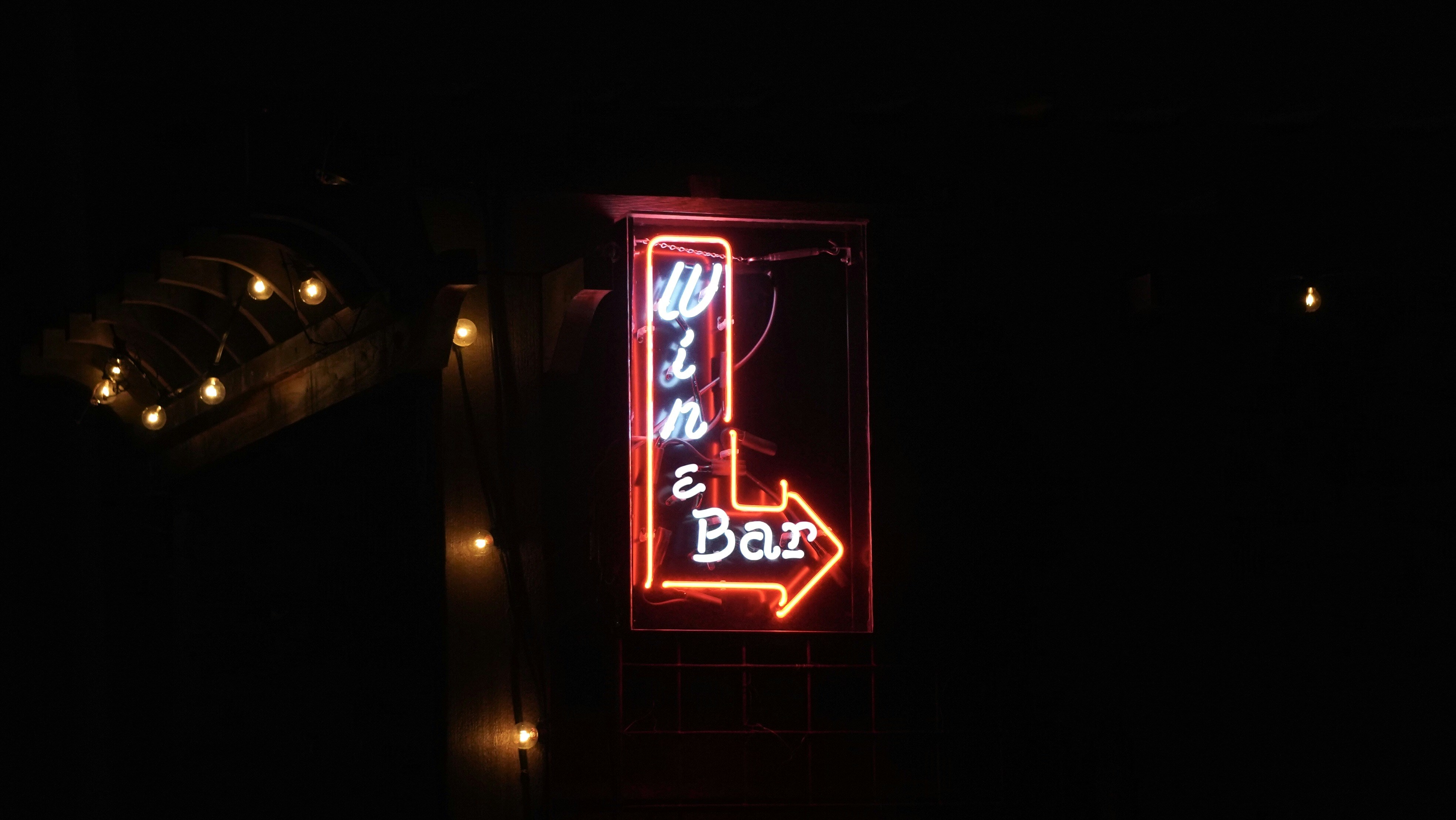 Crimson Neon Wine Bar Sign in a Dim Window, Framed by Warm String Lights