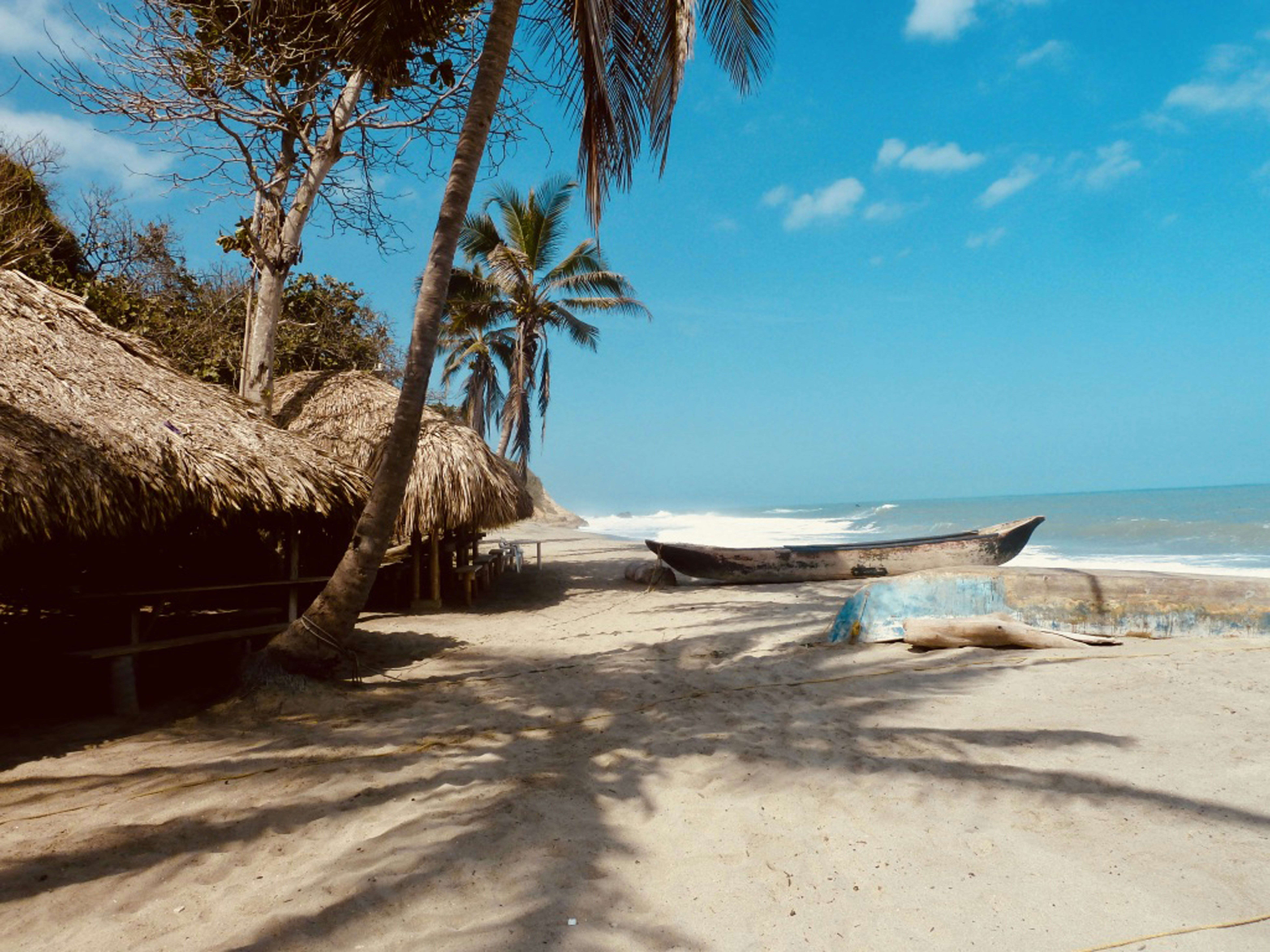 Palm-fringed beach with a rustic boat on the sand under a clear blue sky.