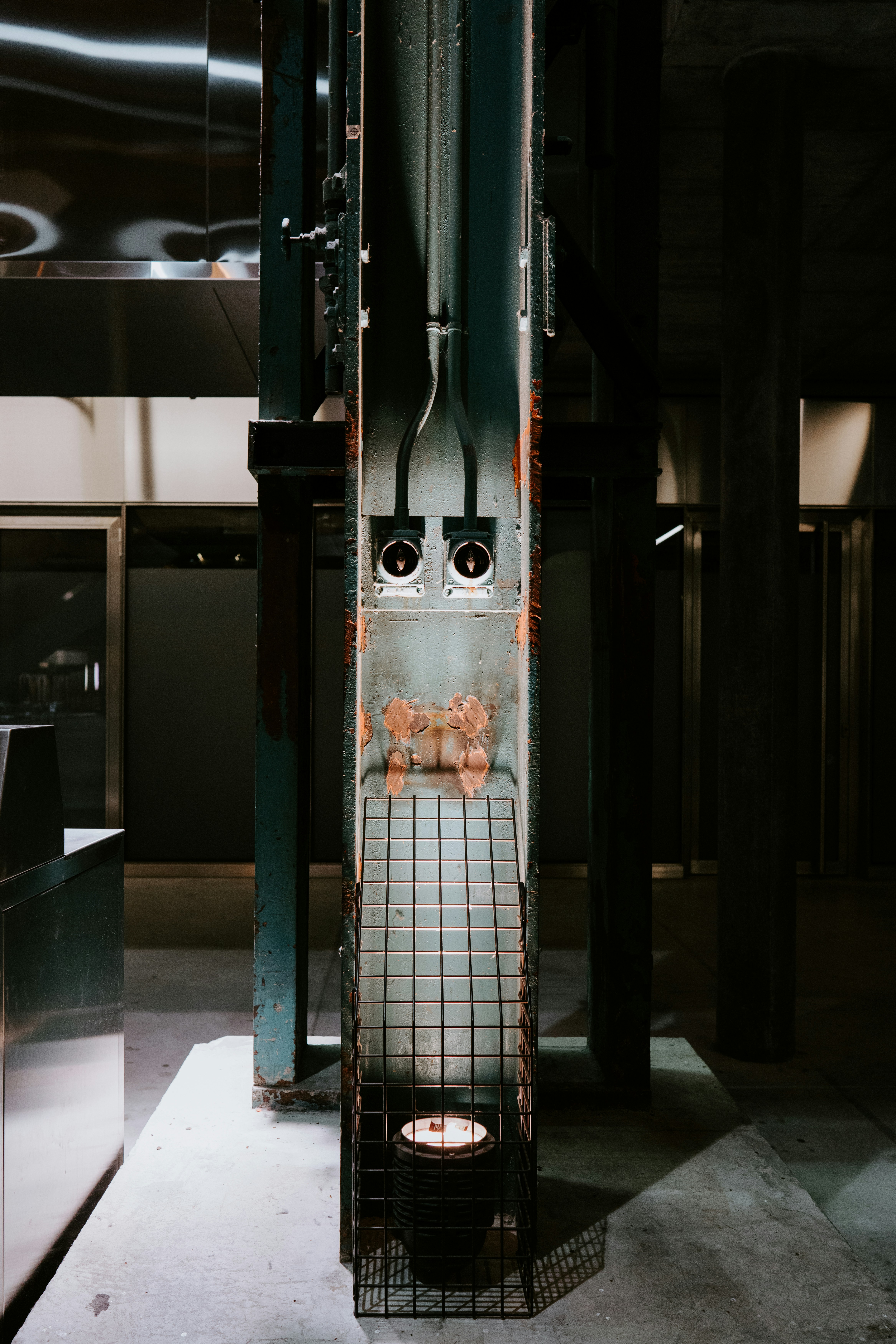 A weathered metal structure with an abstract face, illuminated by soft light, standing in a modern industrial space.