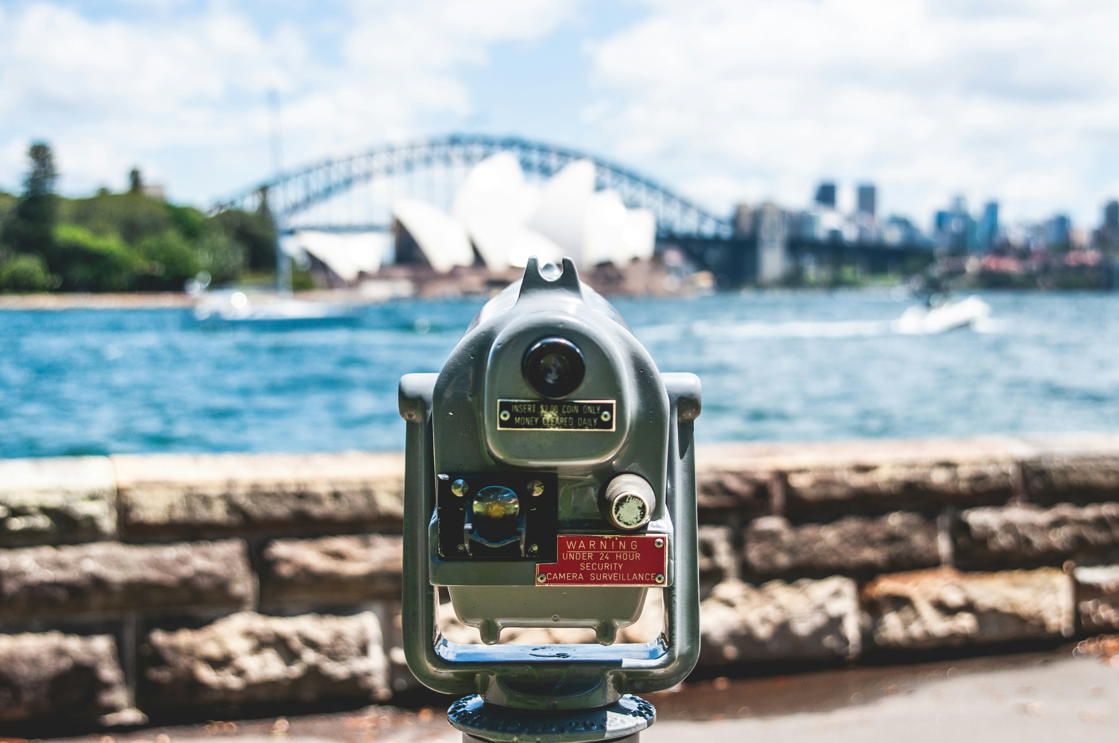Coin-operated telescope overlooking the Sydney Opera House and Harbour Bridge, with boats gliding across the water.