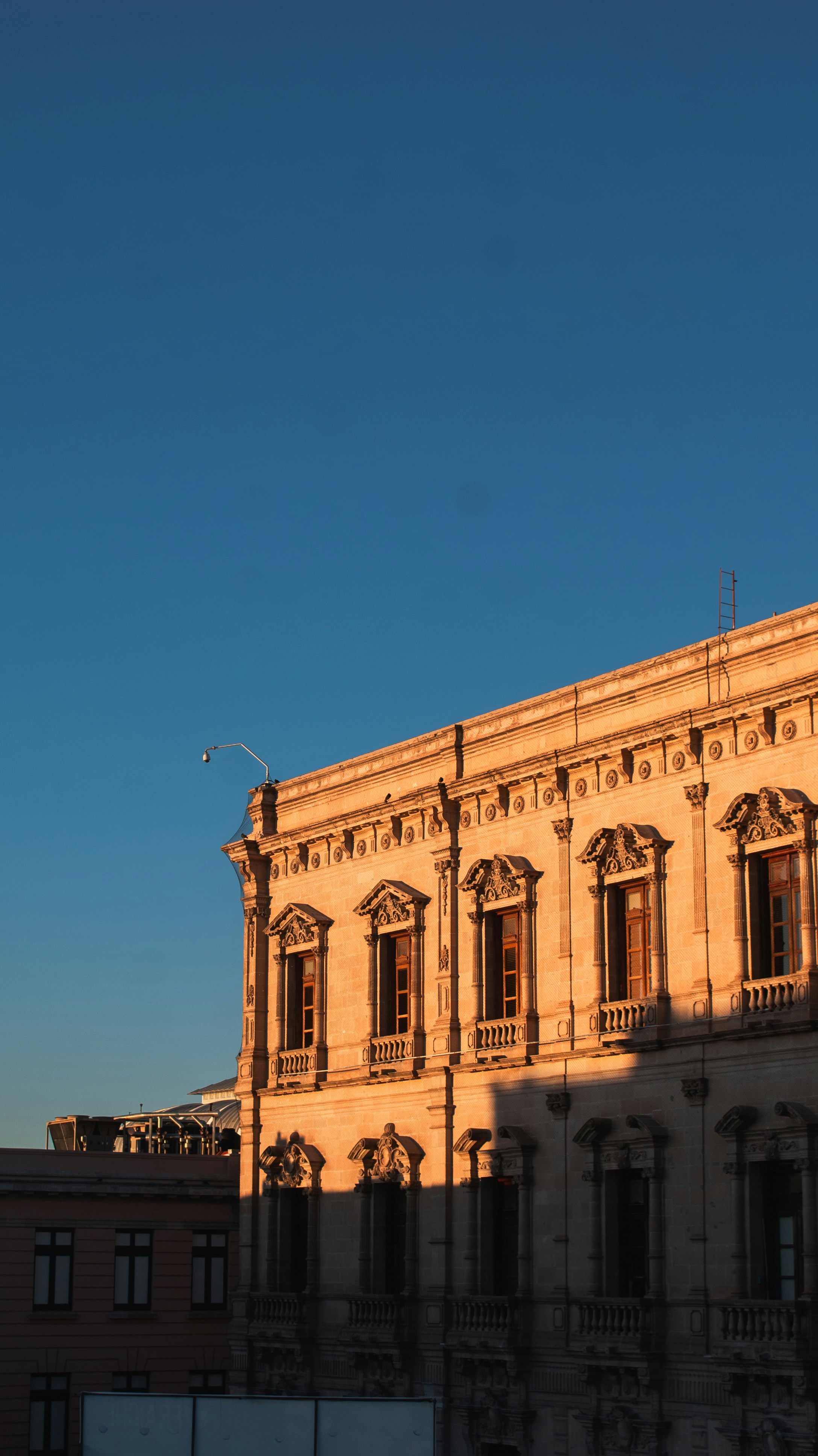 Historic building bathed in warm sunlight with ornate windows against a clear blue sky.