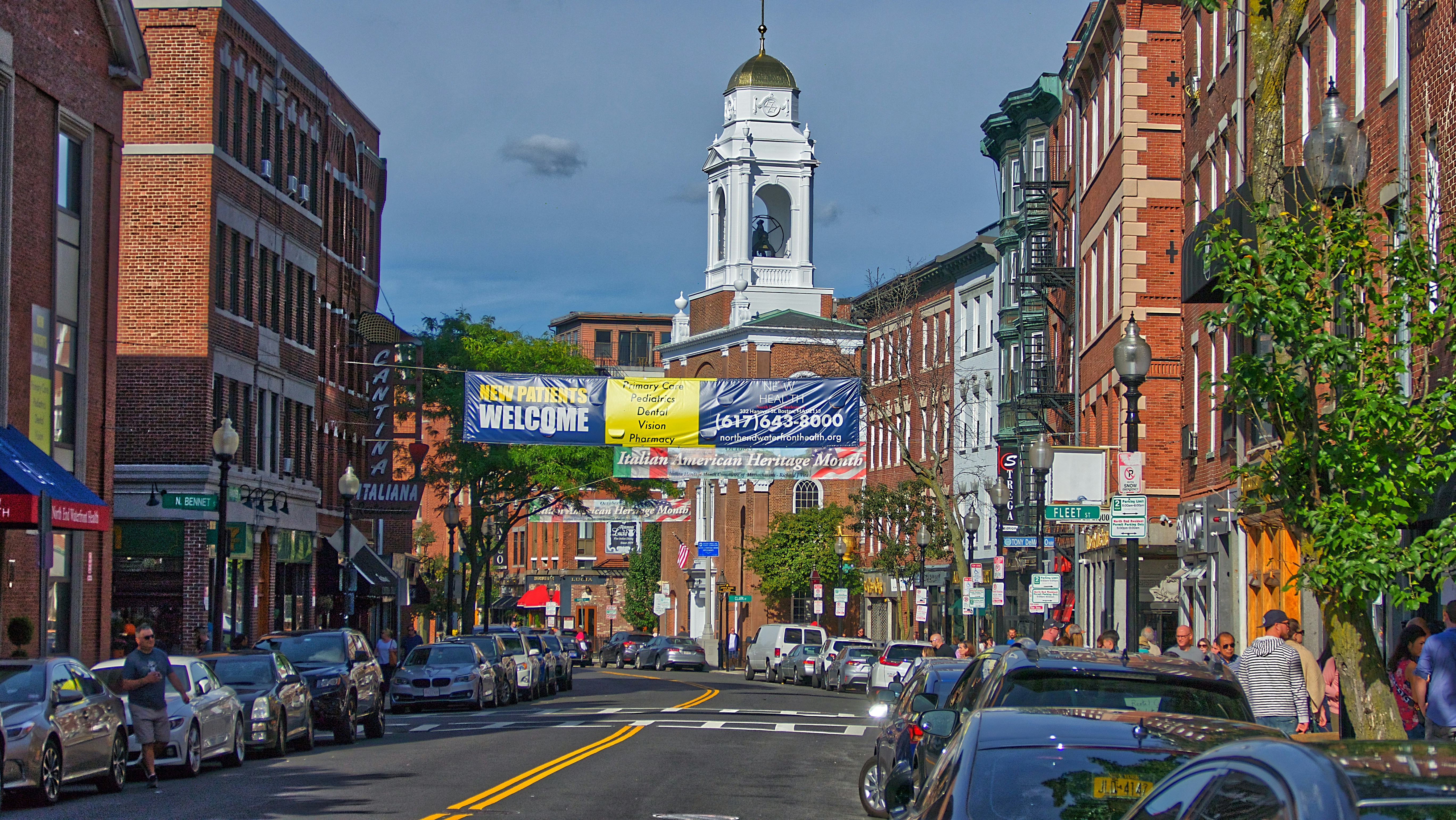 Street view of St. Stephen's Church with its prominent white tower framed by historic brick buildings and bustling city life.