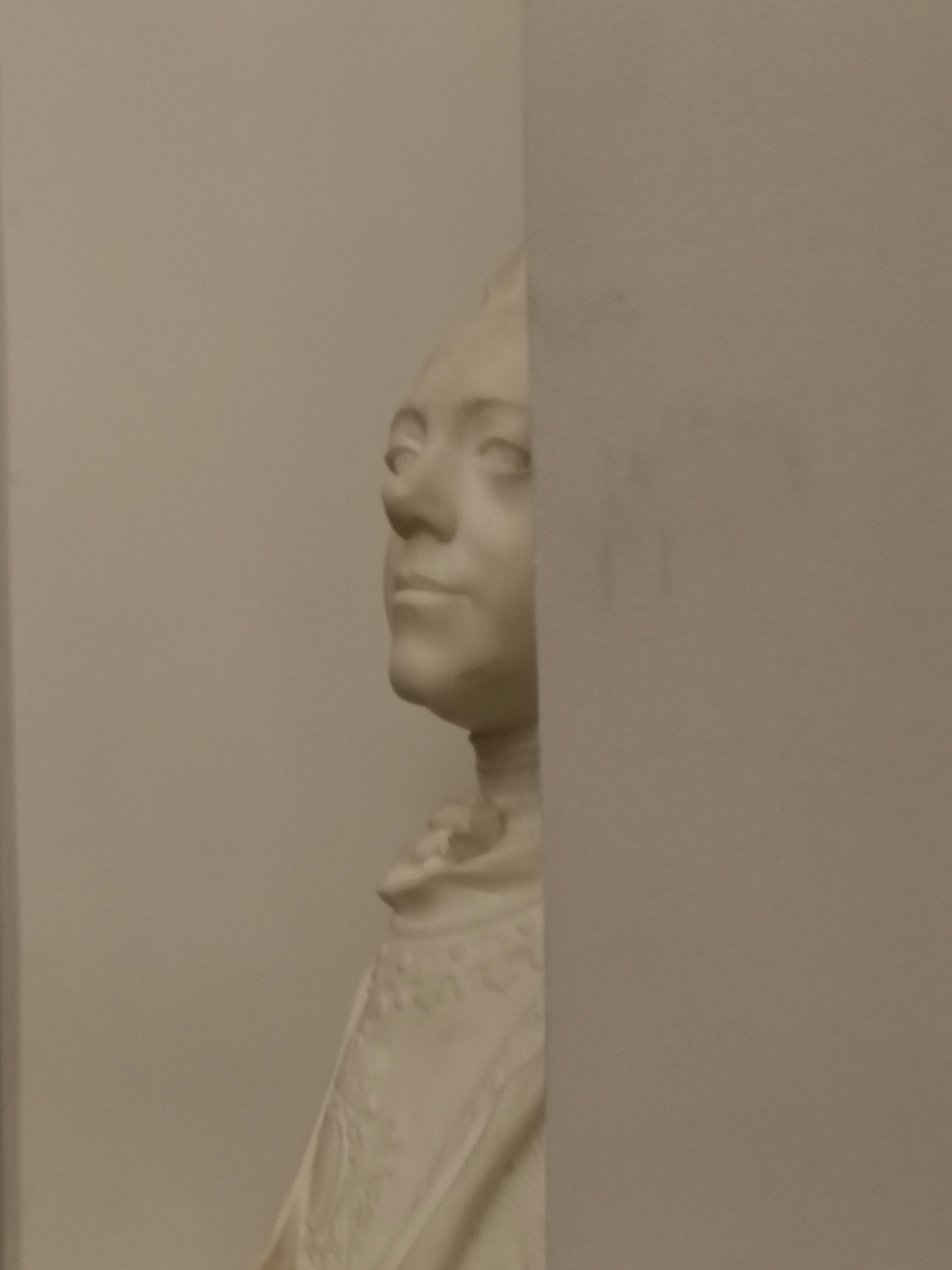 A sculpted figure partially obscured by a wall, capturing a moment of contemplation and mystery.