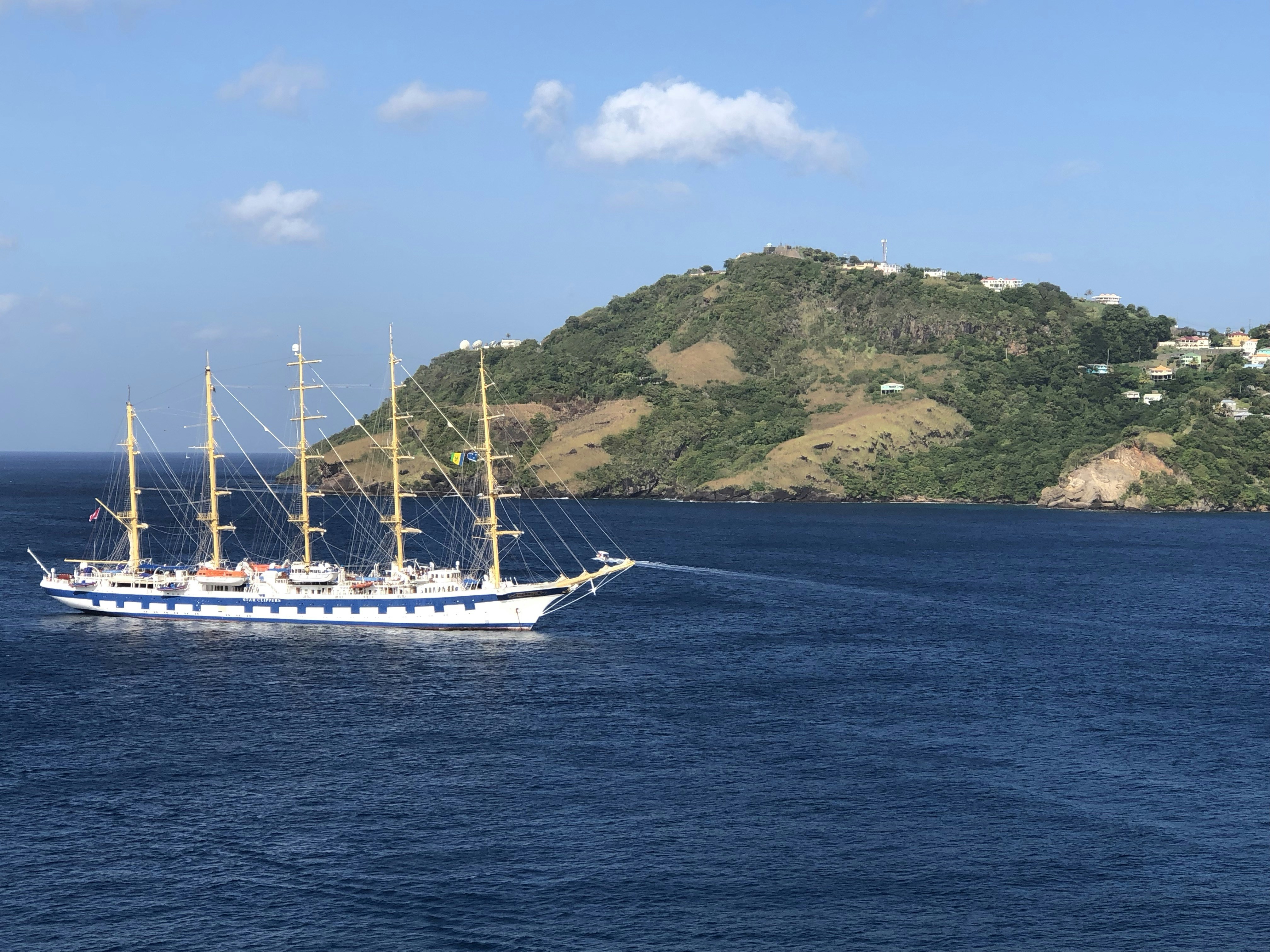 A majestic tall ship navigates the deep blue waters near a lush green island, showcasing the harmony between sea and land.