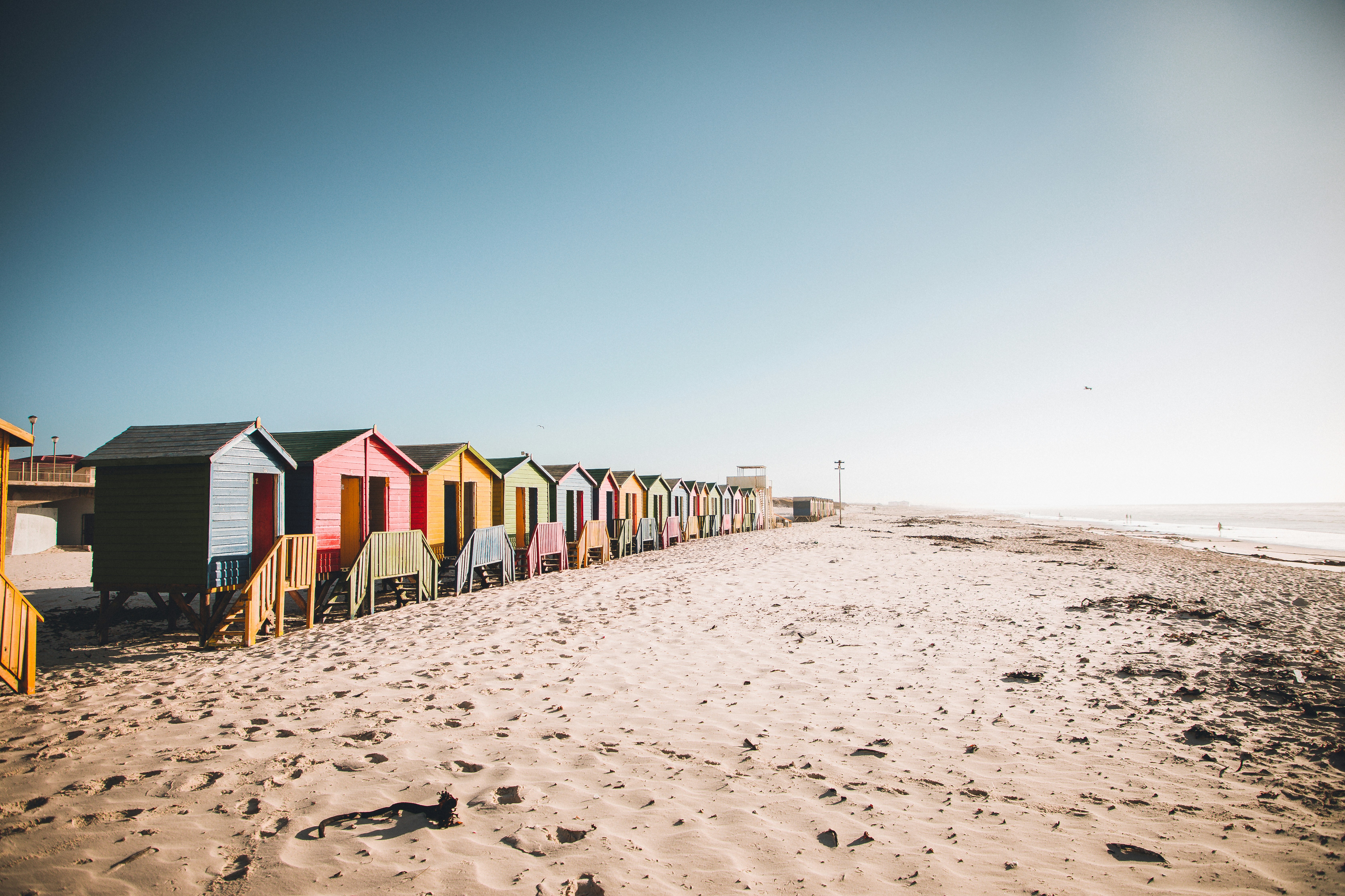 Colorful beach huts line the sandy expanse under a clear sky.