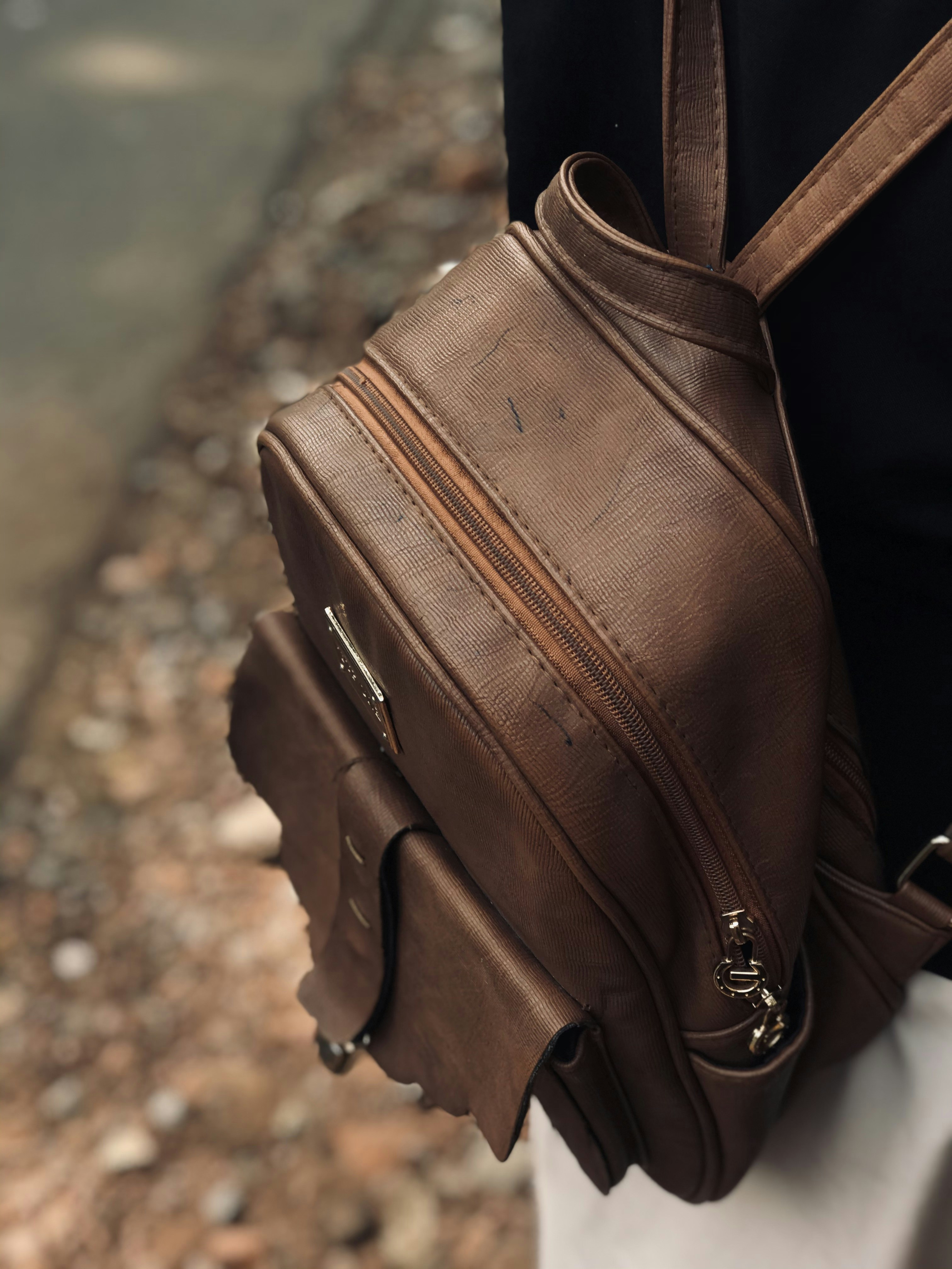Leather-stitched Traveler: a close-up of a brown backpack along a leaf-strewn path