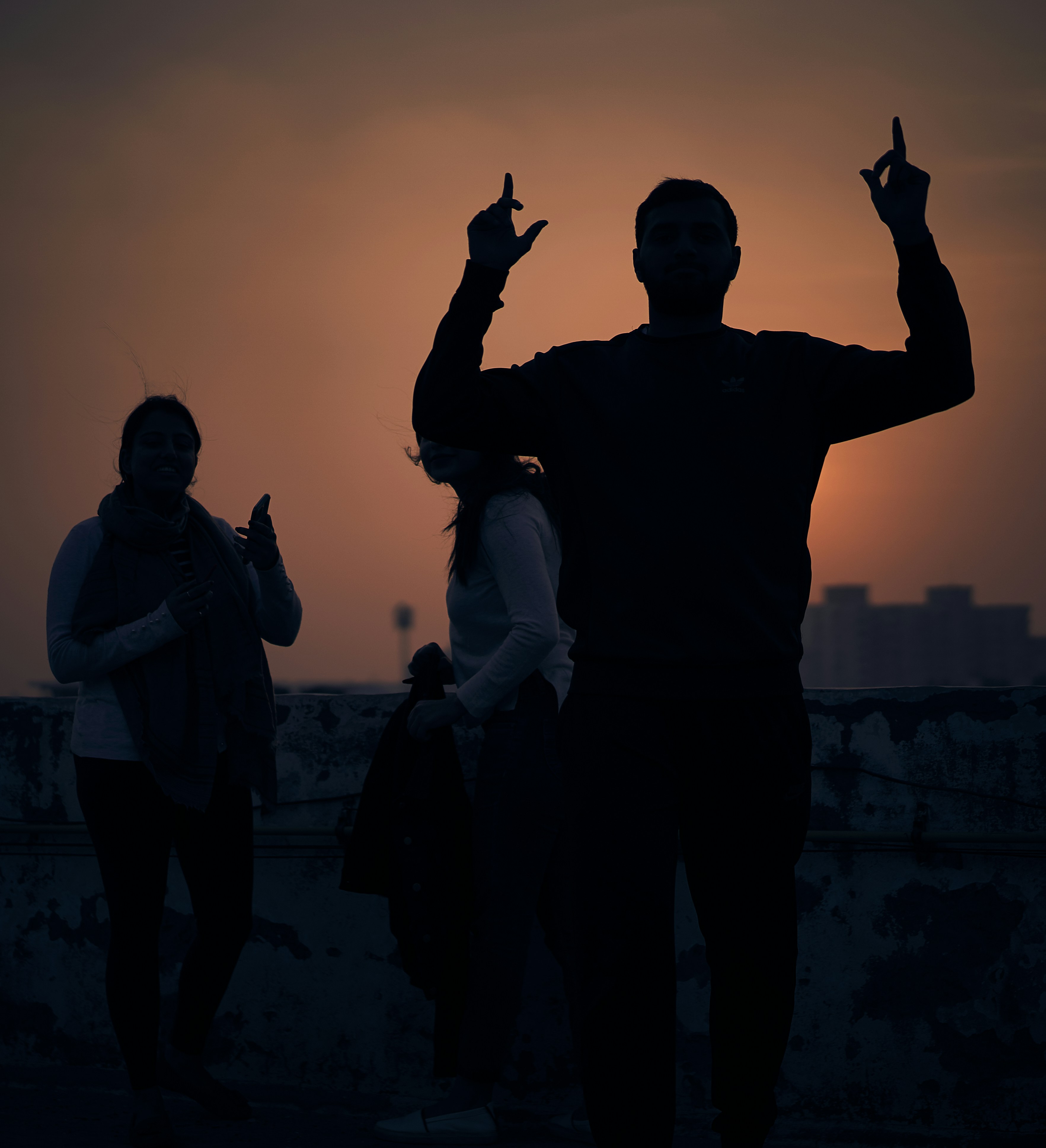 Rooftop Dusk: Central Silhouette Raising a Rock Sign Against an Orange Horizon
