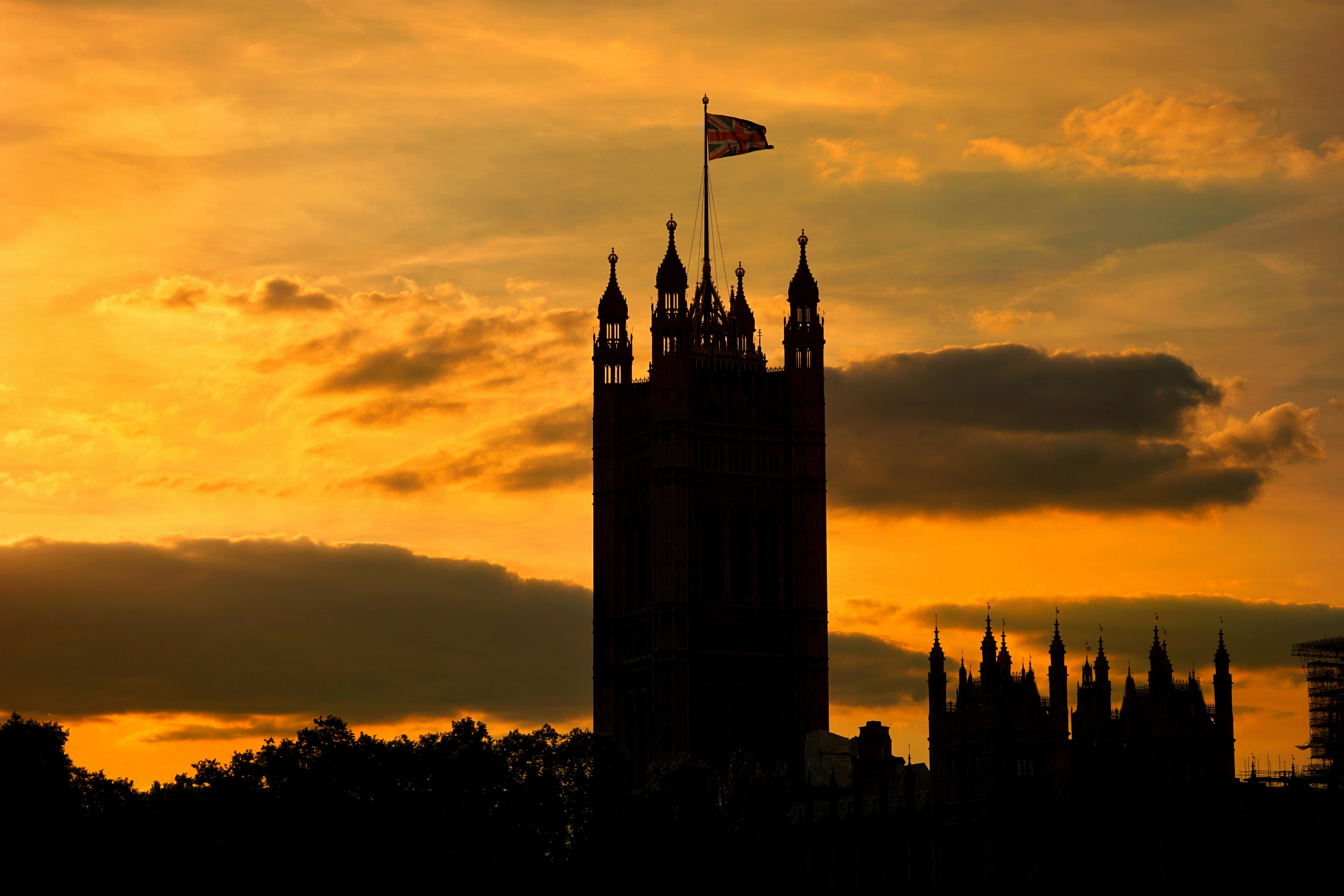 The silhouette of the iconic Palace of Westminster against a vibrant sunset sky, with the Union Jack fluttering atop its tower.