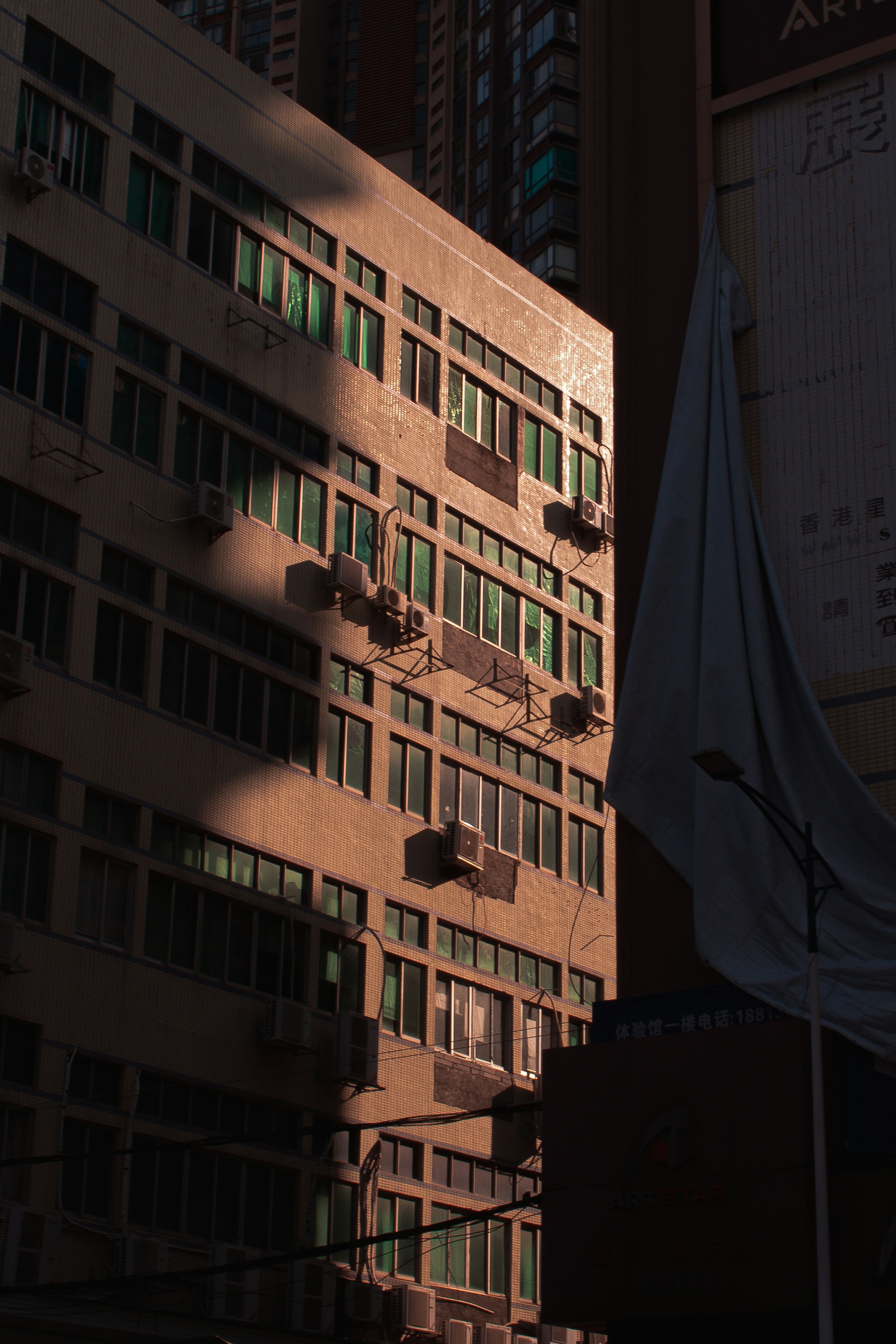Sunlight casts intriguing shadows on a textured building facade adorned with air conditioning units, highlighting the interplay of light and architecture.