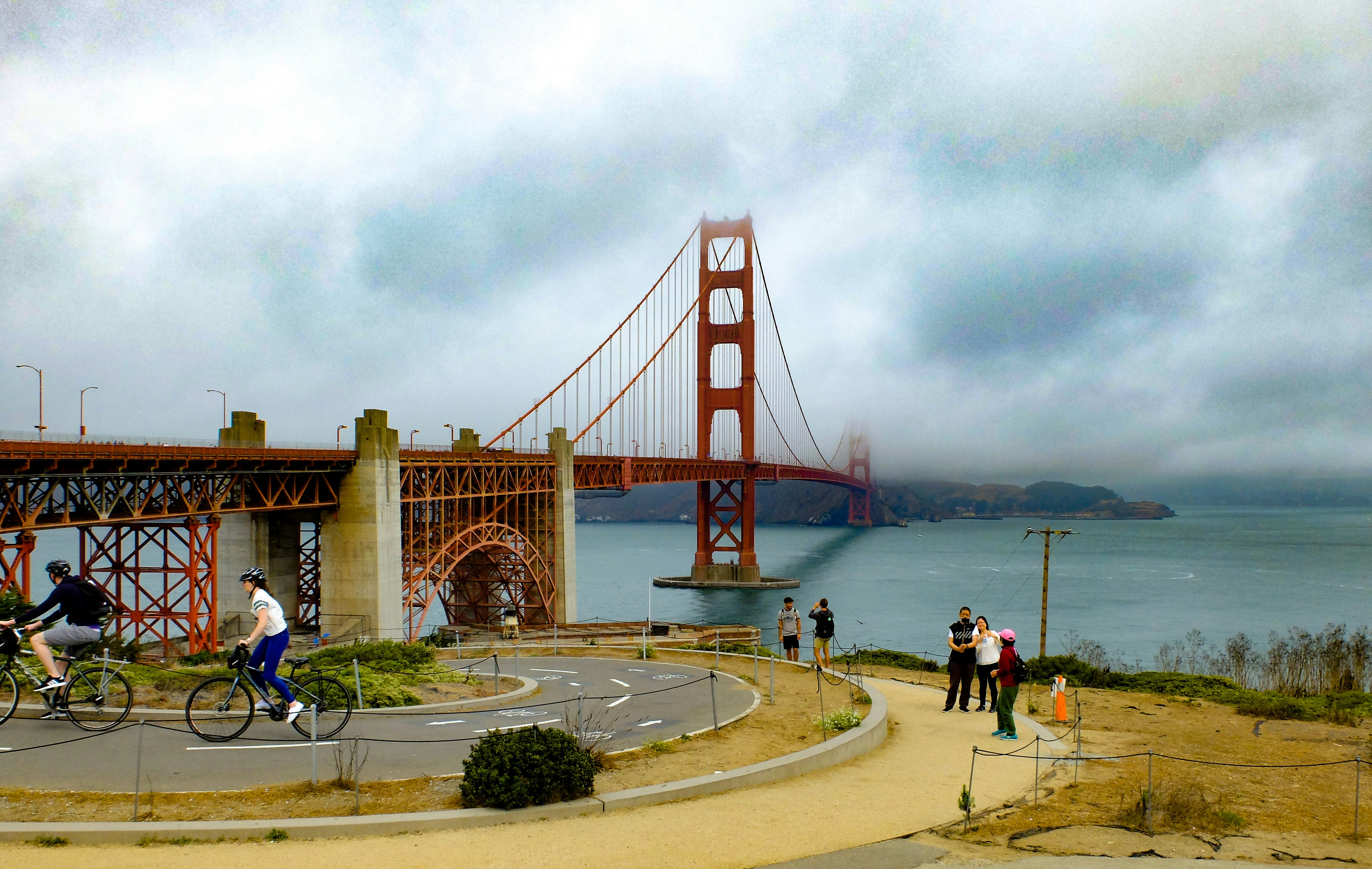 Amber Arc Beneath the Golden Gate Bridge: Cyclists, Curve, and Bay