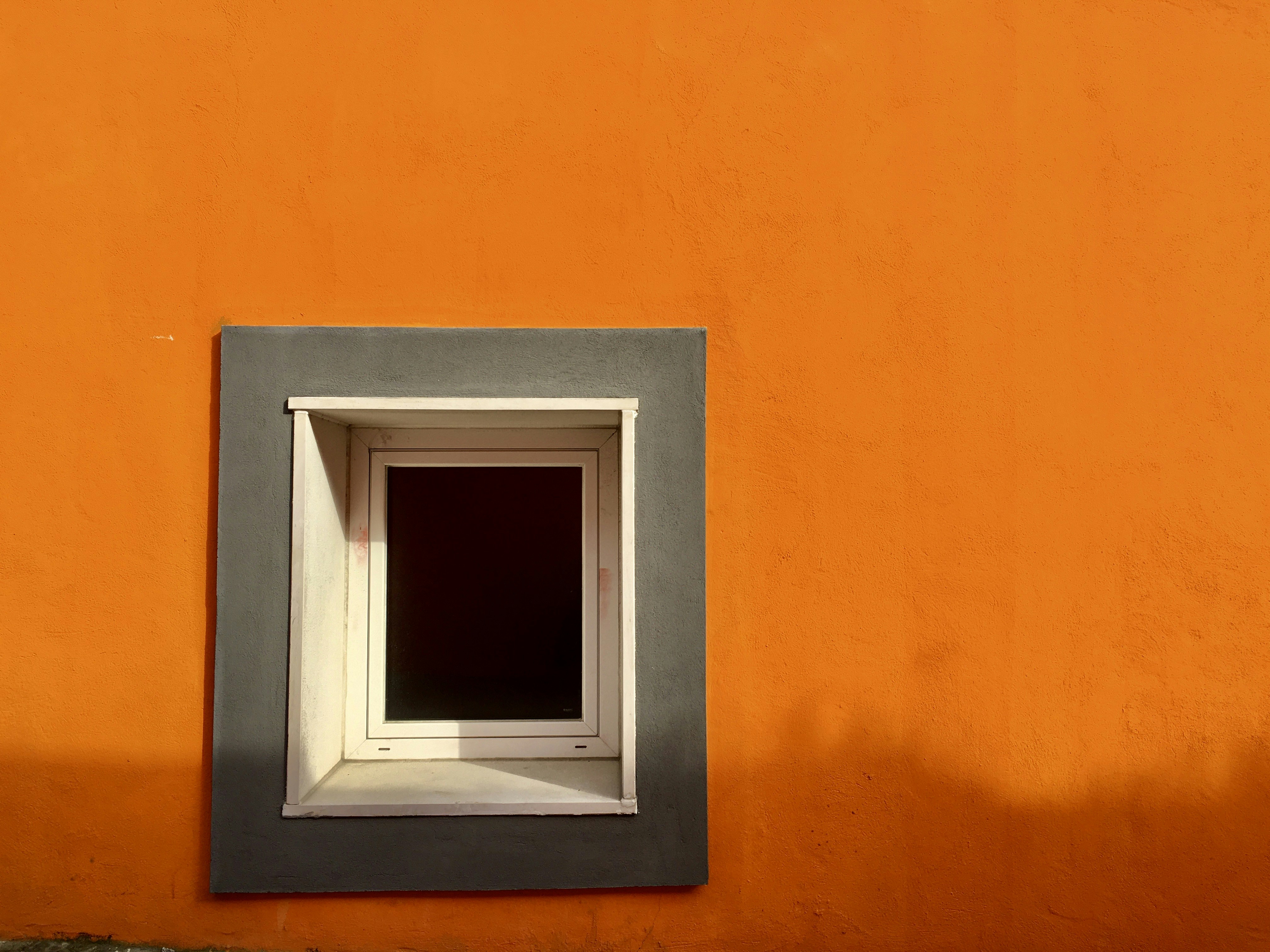 A minimalist window set against a vibrant orange wall, showcasing a stark contrast between the geometric shapes and colors.