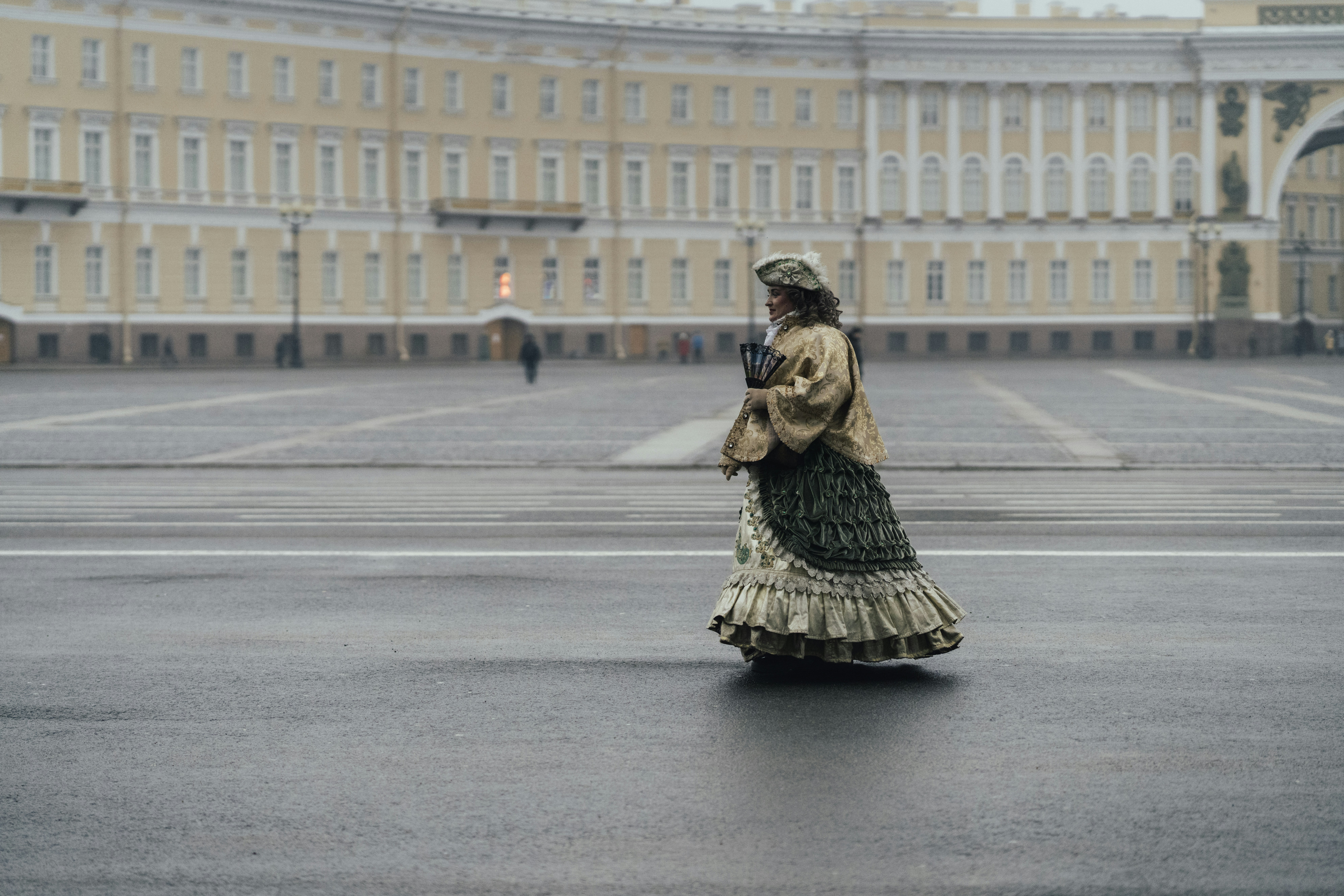 Woman in period attire walking across a grand, empty plaza with ornate architecture in the background.