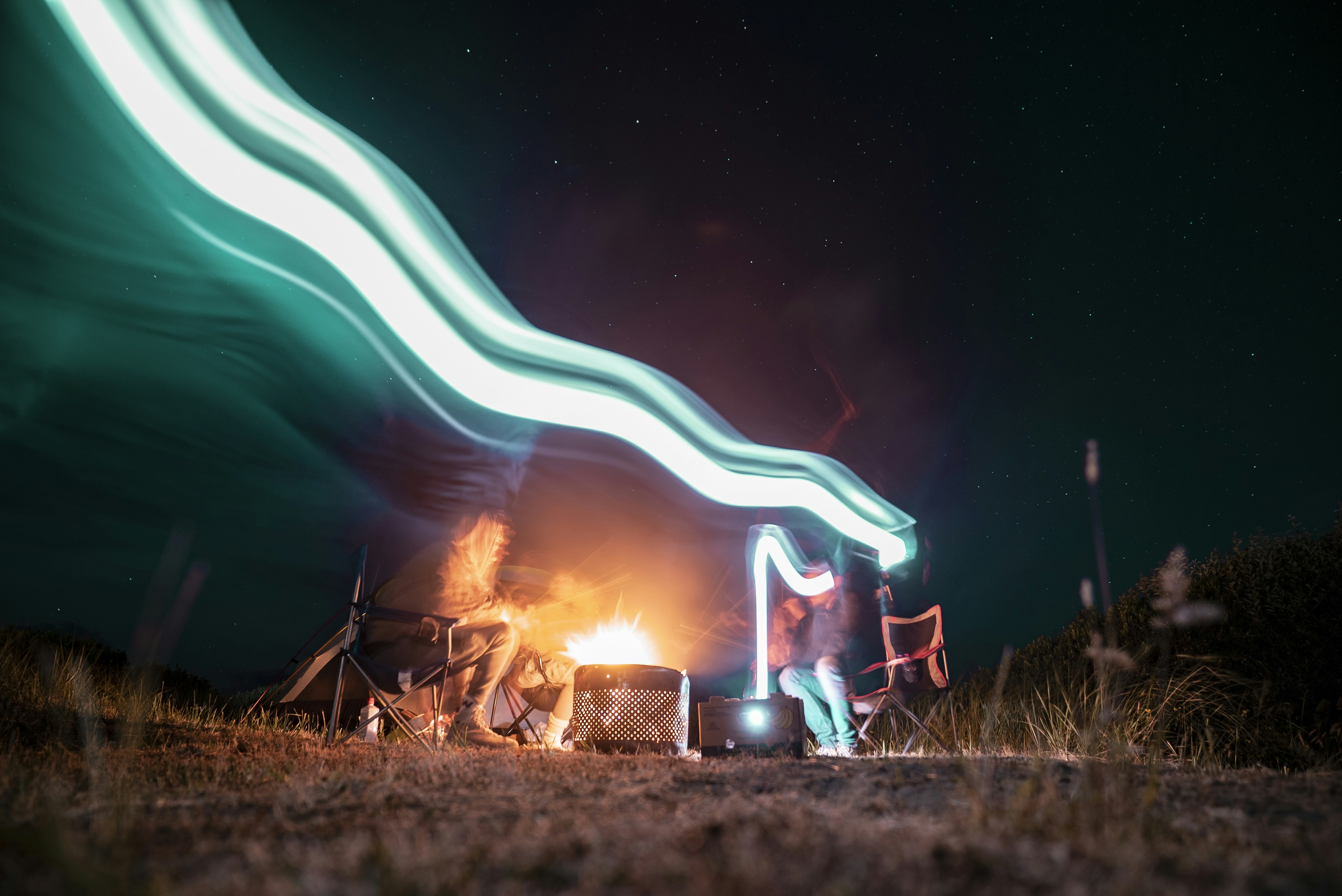 Neon Arc Over a Night Campsite: Light Trails Sweep the Campfire