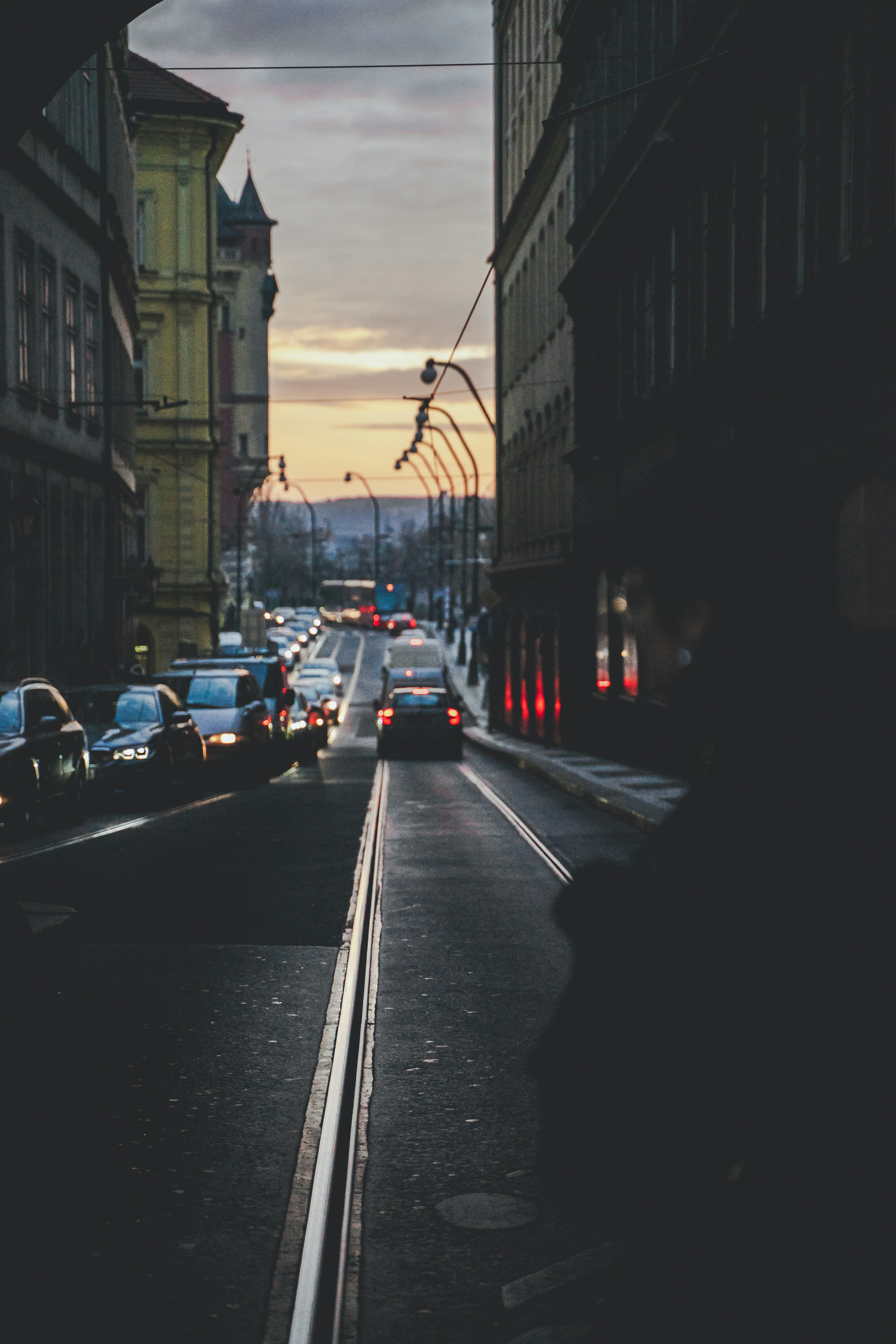 A city street at twilight, with cars navigating a sloped road under an archway, showcasing a blend of urban architecture and fading daylight.