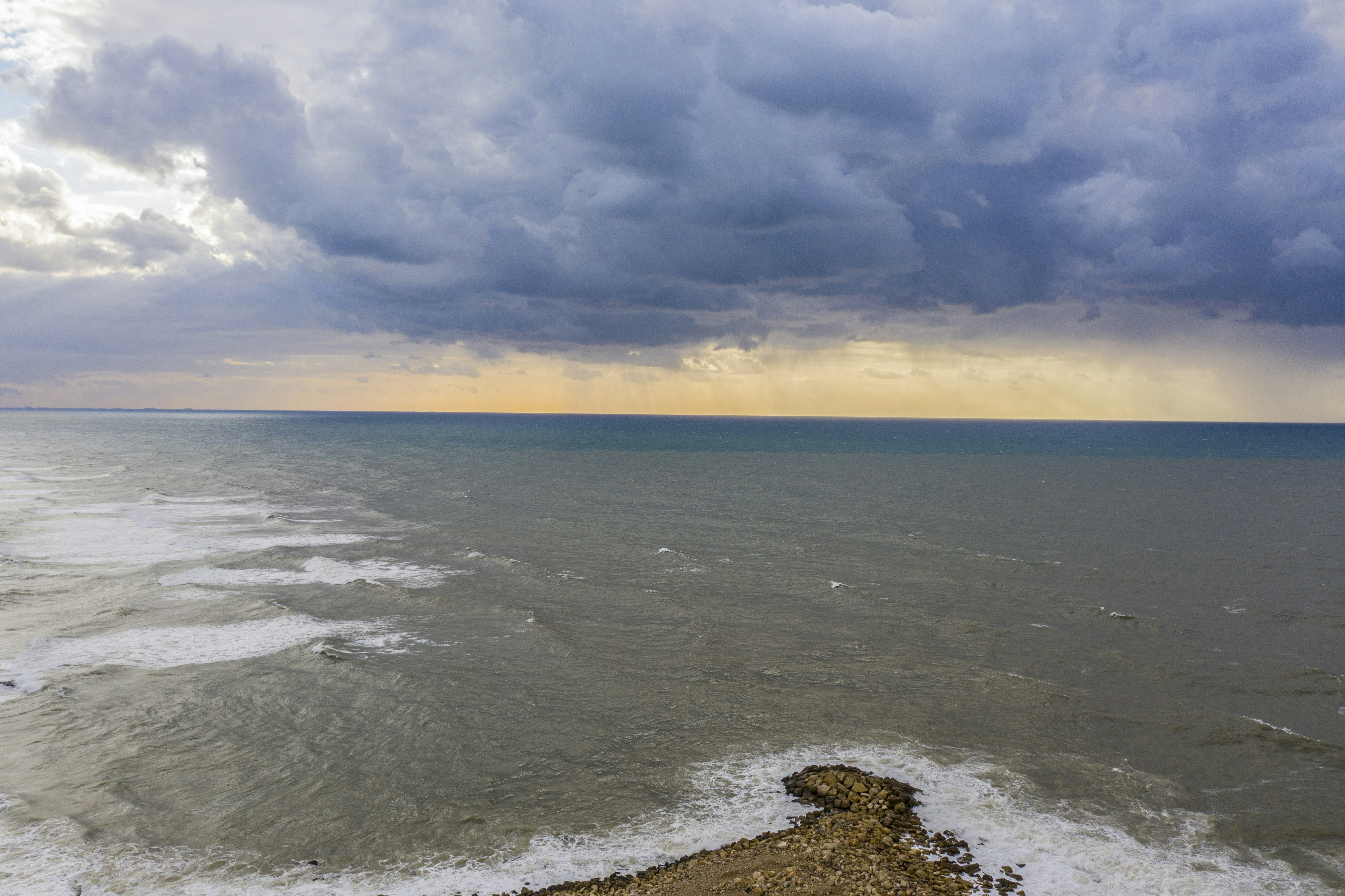 Stormy seascape with turbulent waves crashing against a rocky shore, illuminated by soft light from the horizon.