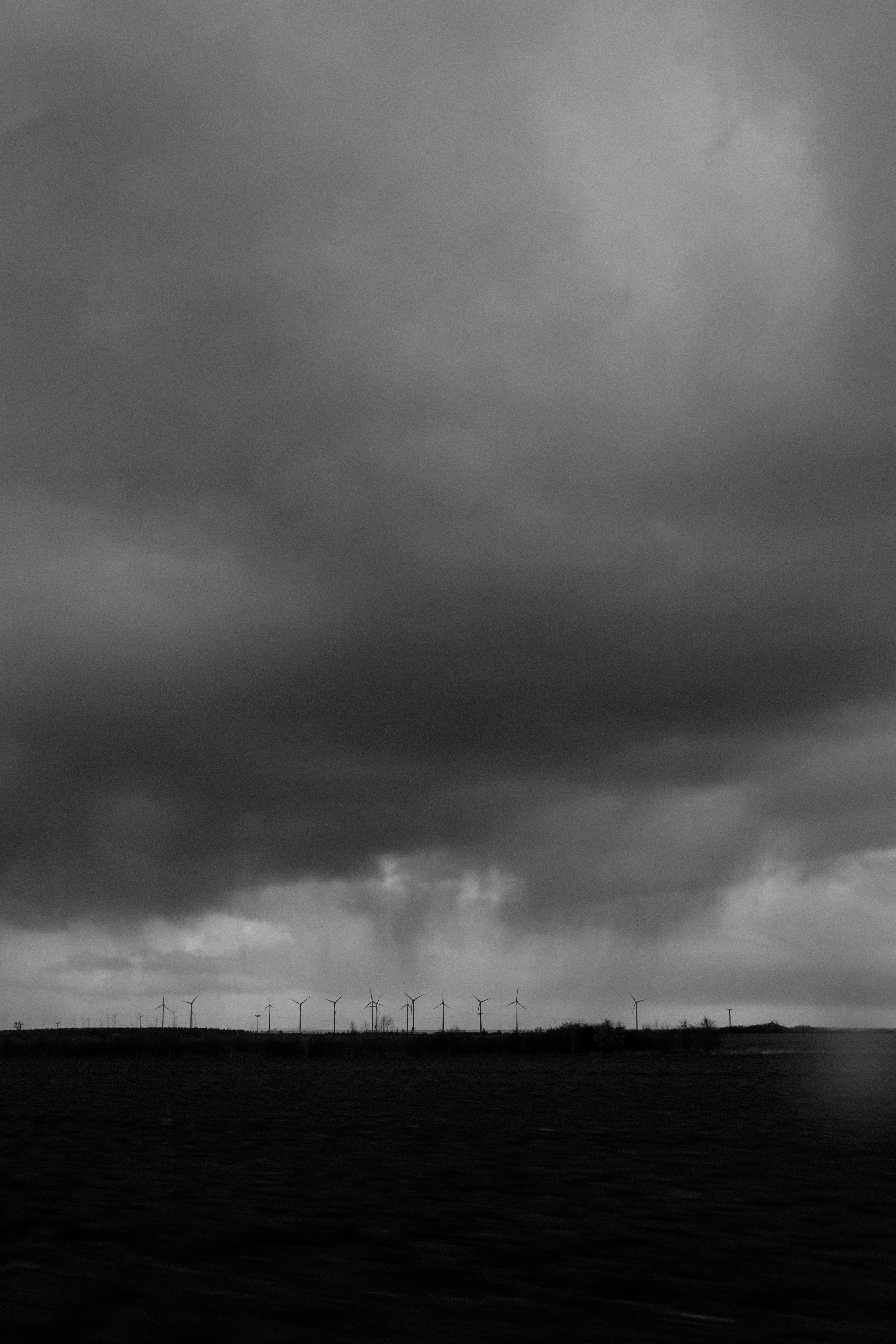 Dark clouds loom over a distant line of wind turbines, creating a dramatic contrast against the water's surface. The scene evokes a sense of impending weather.