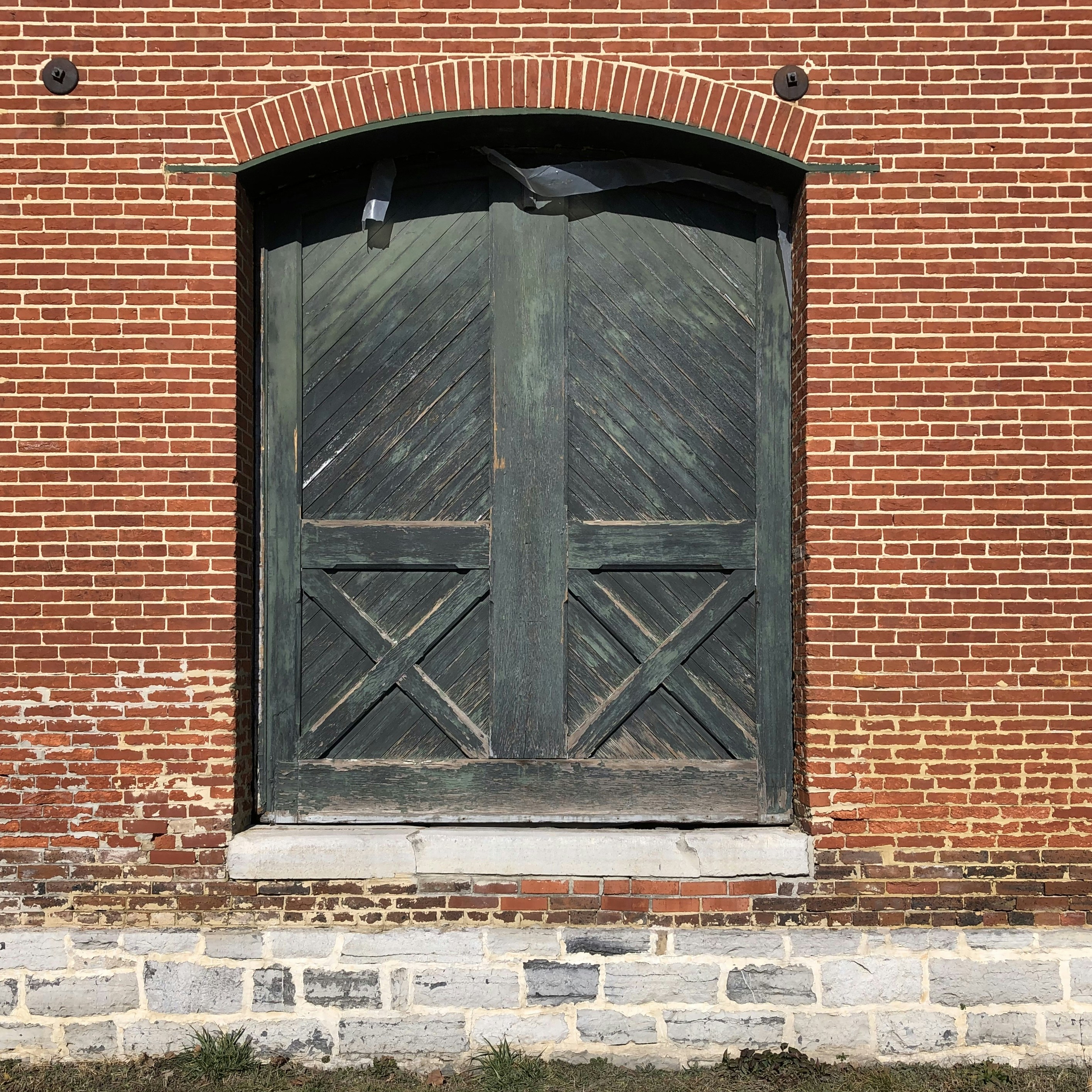 Weathered green double doors set against a brick wall, showcasing rustic charm and historical significance.