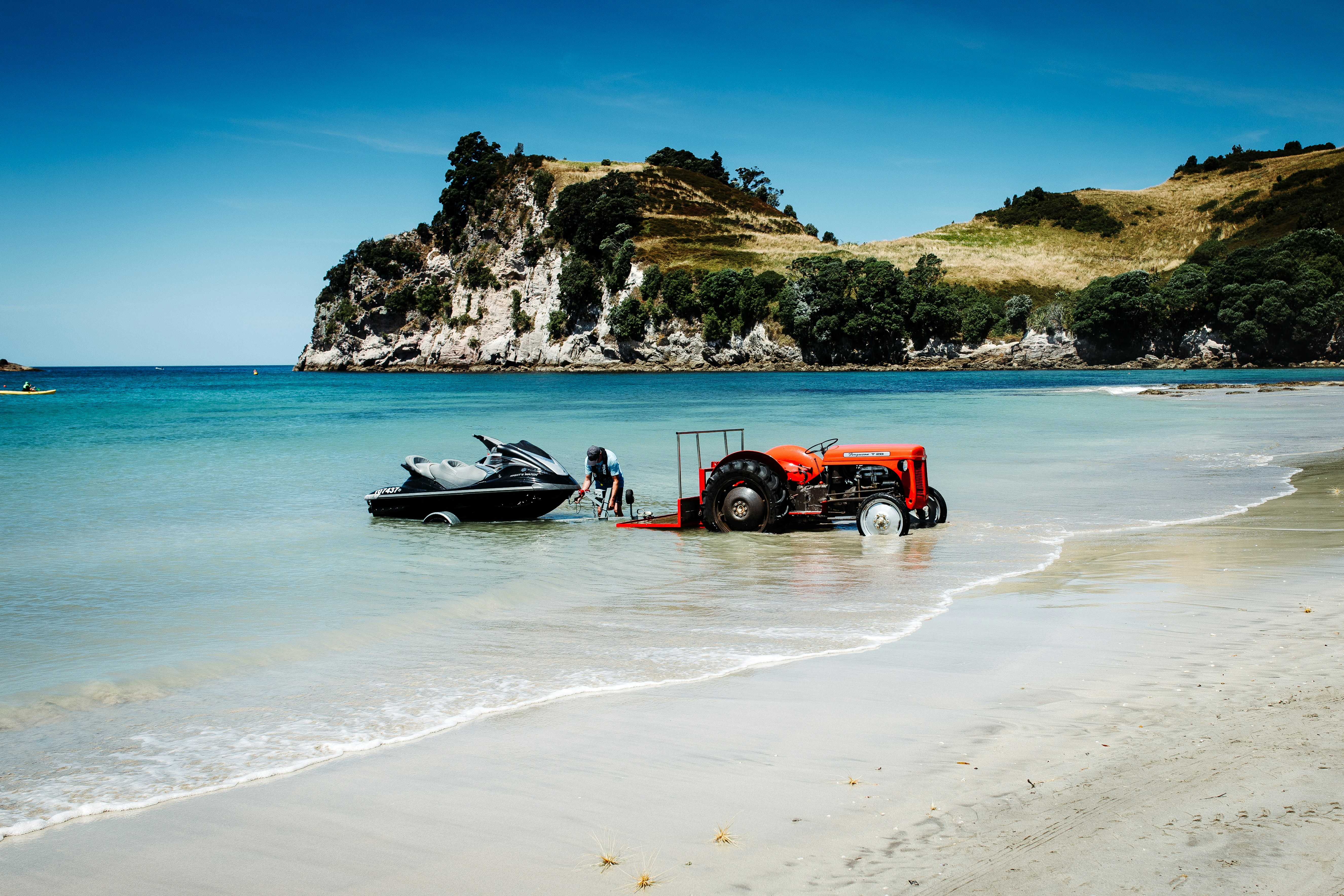 Shoreline Convoy: Red Tractor Anchored on Turquoise Sands