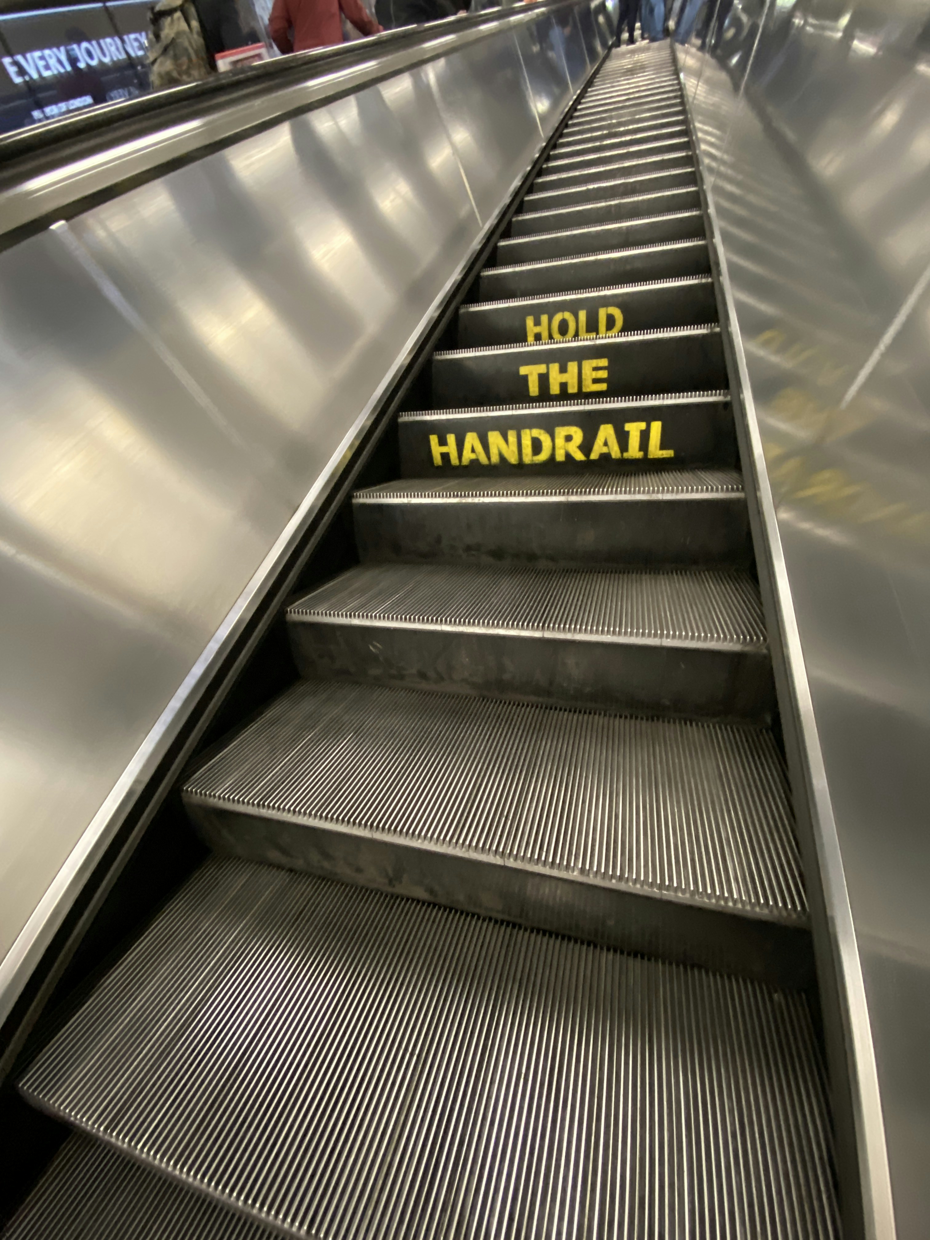 Yellow warning text reading 'HOLD THE HANDRAIL' on escalator steps, emphasizing safety in public spaces.