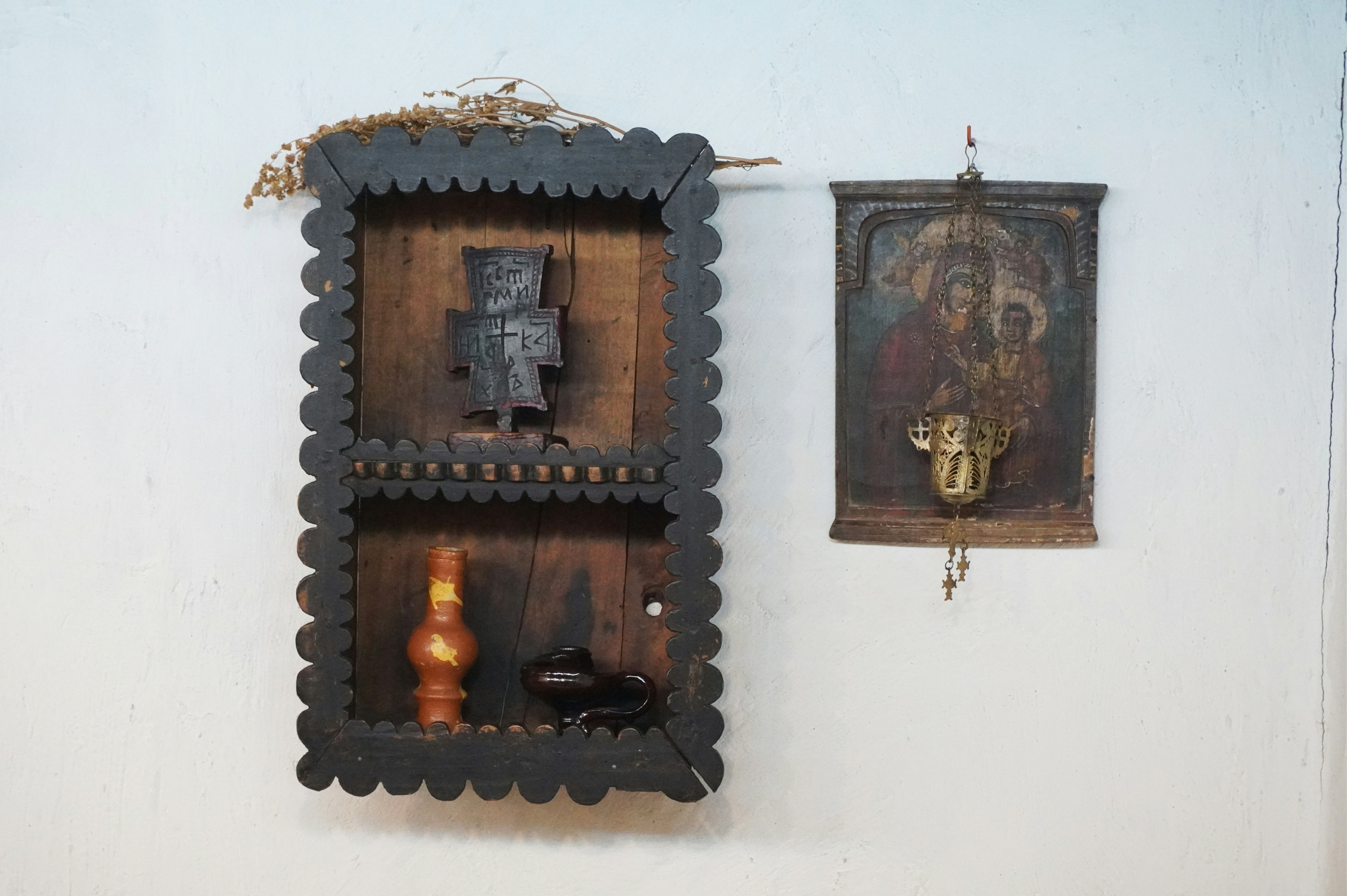 A Quiet Shrine on a Pale Wall: Scalloped reliquary frames a small cross beside a weathered icon