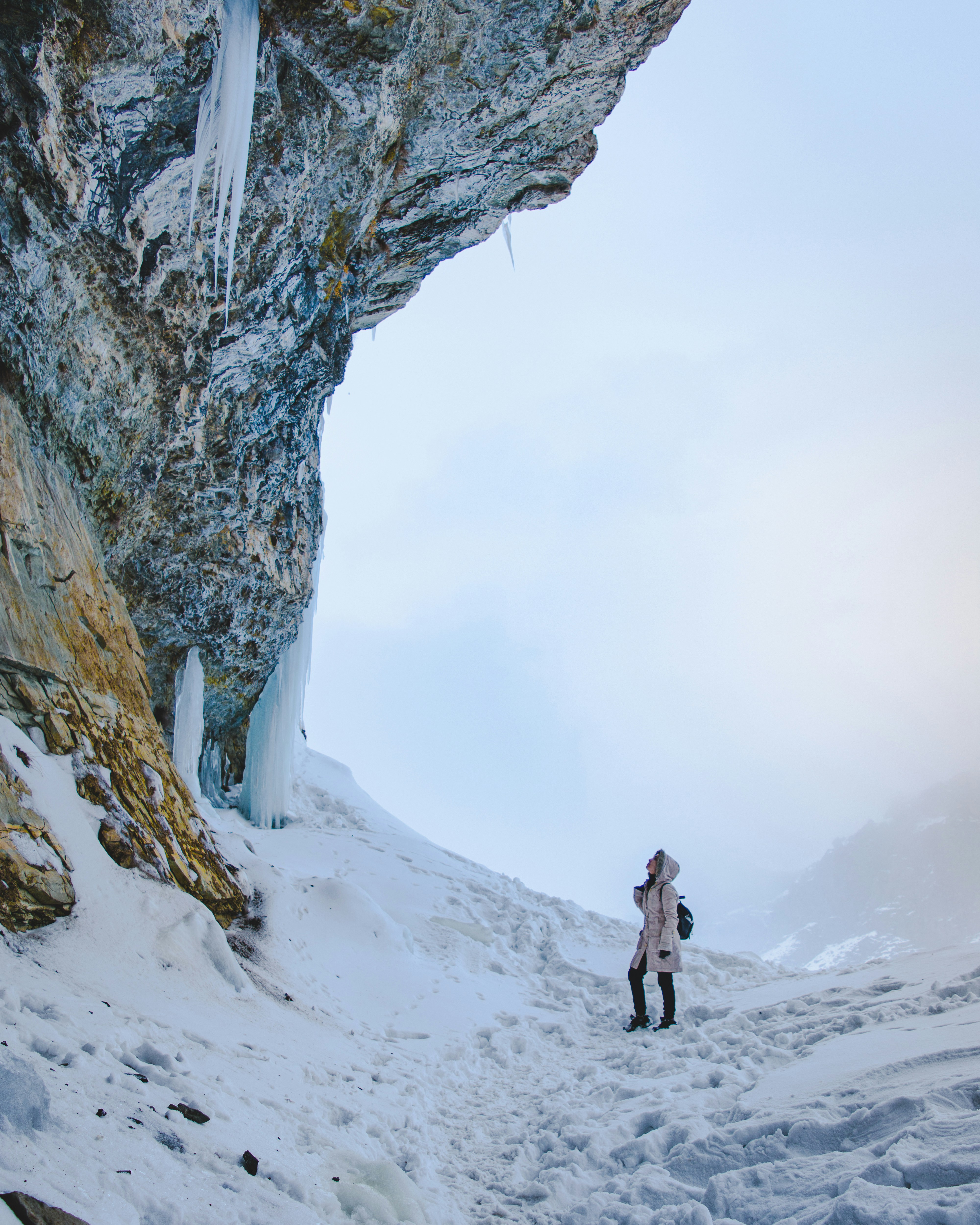 Lone Traveler on a Frosty Slope Beneath an Icicle-Crowned Cliff