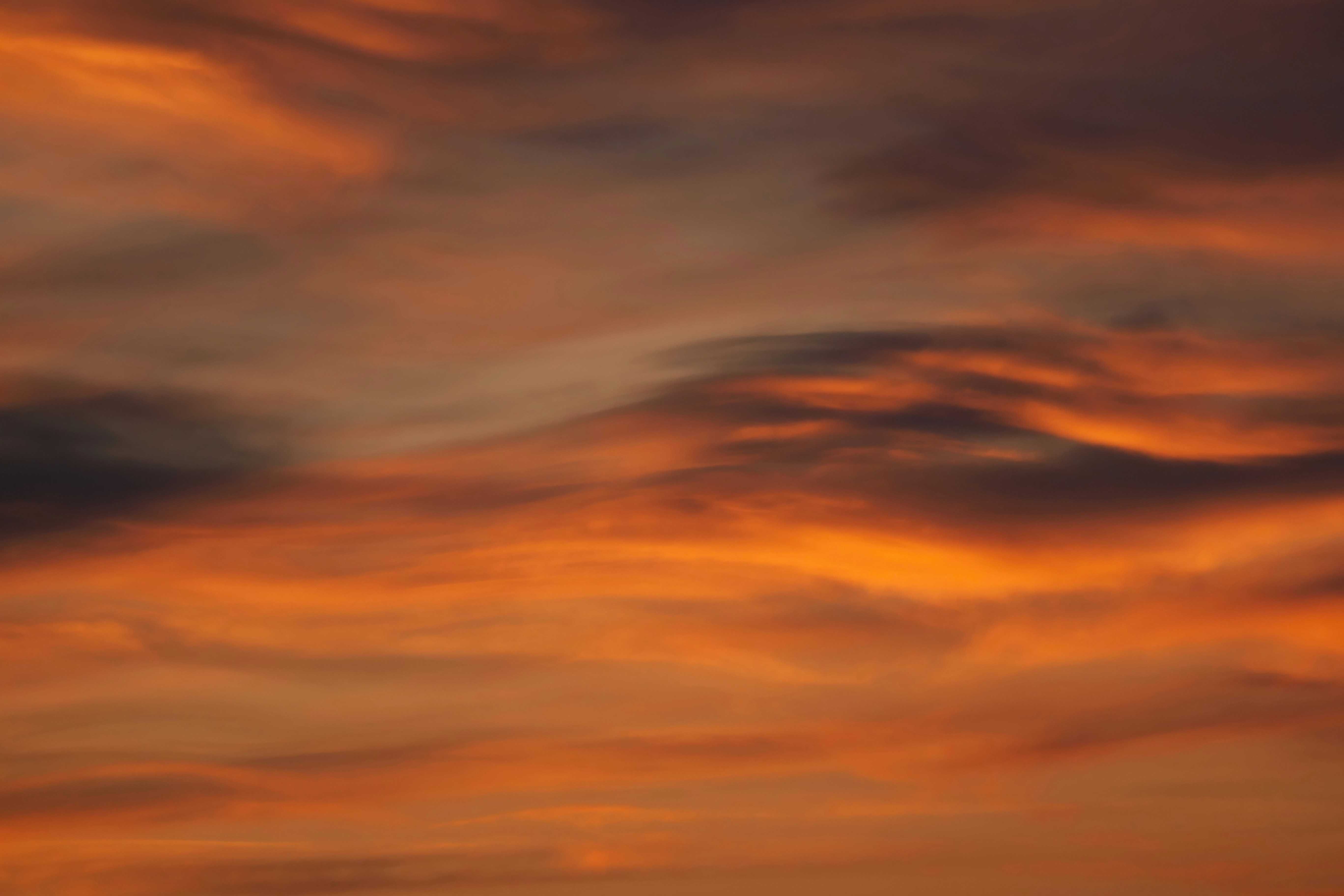 Vibrant orange and red clouds swirl against a darkening sky at sunset.
