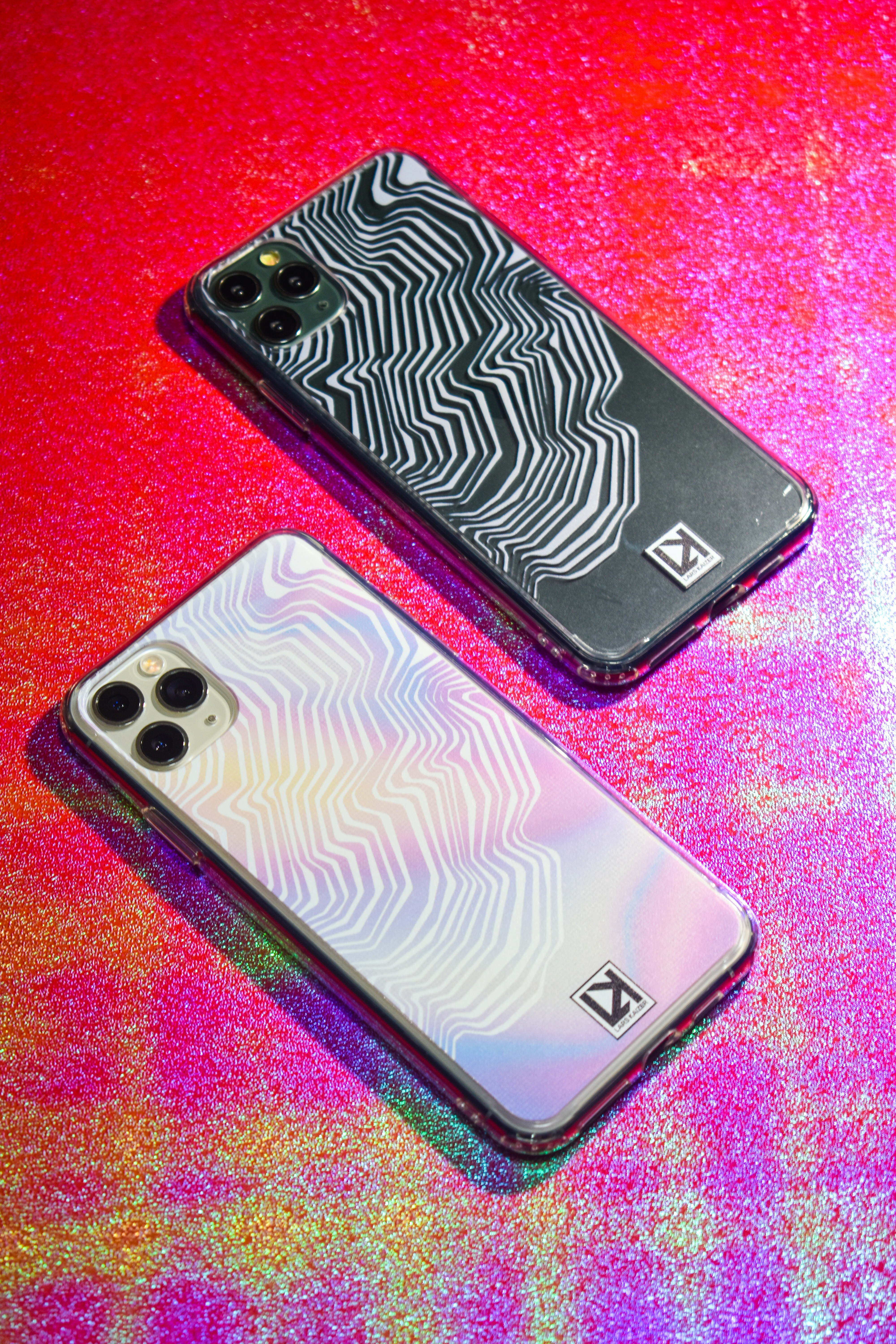 Two smartphone cases with intricate line designs resting on a vibrant, reflective surface, showcasing a blend of modern aesthetics and color play.