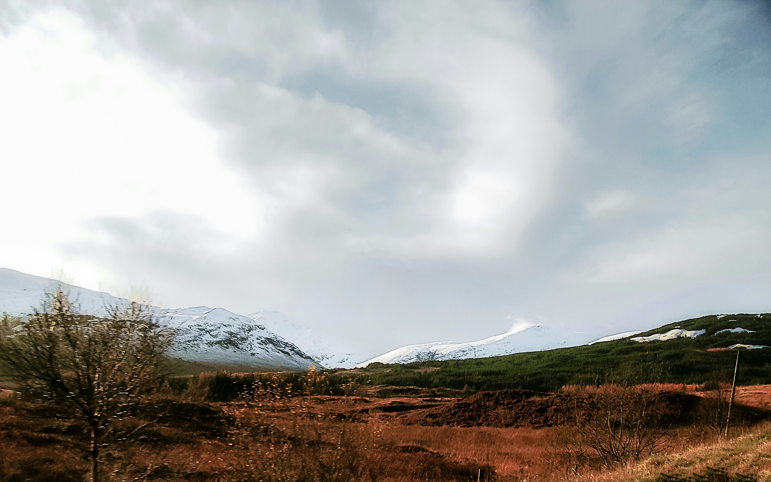 Snow-capped mountains loom over a vibrant, earthy terrain under a cloudy sky. The scene captures the tranquility of the highlands.