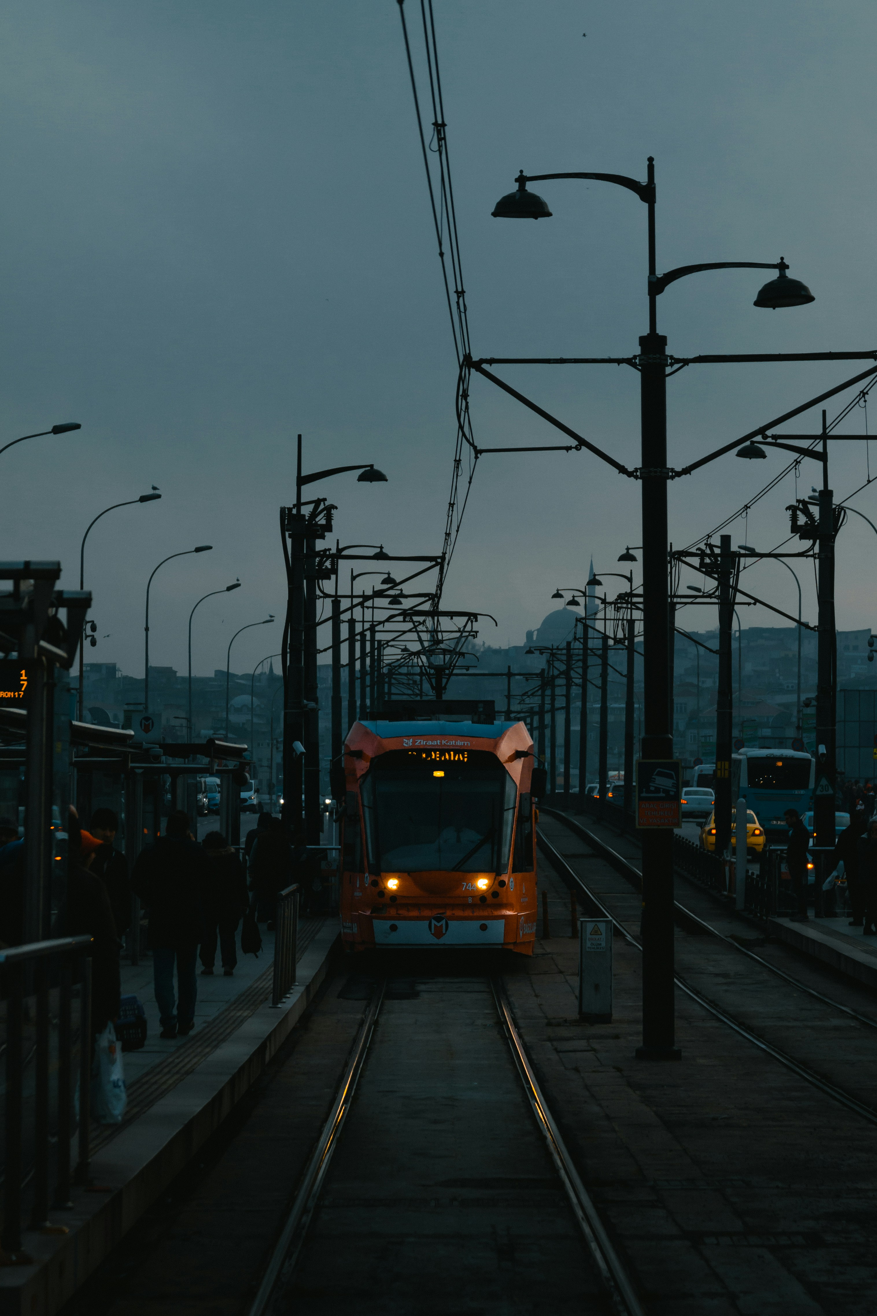 Dusk Tram on a Grid of Rails: An Orange Car Amid Wires and Lanterns