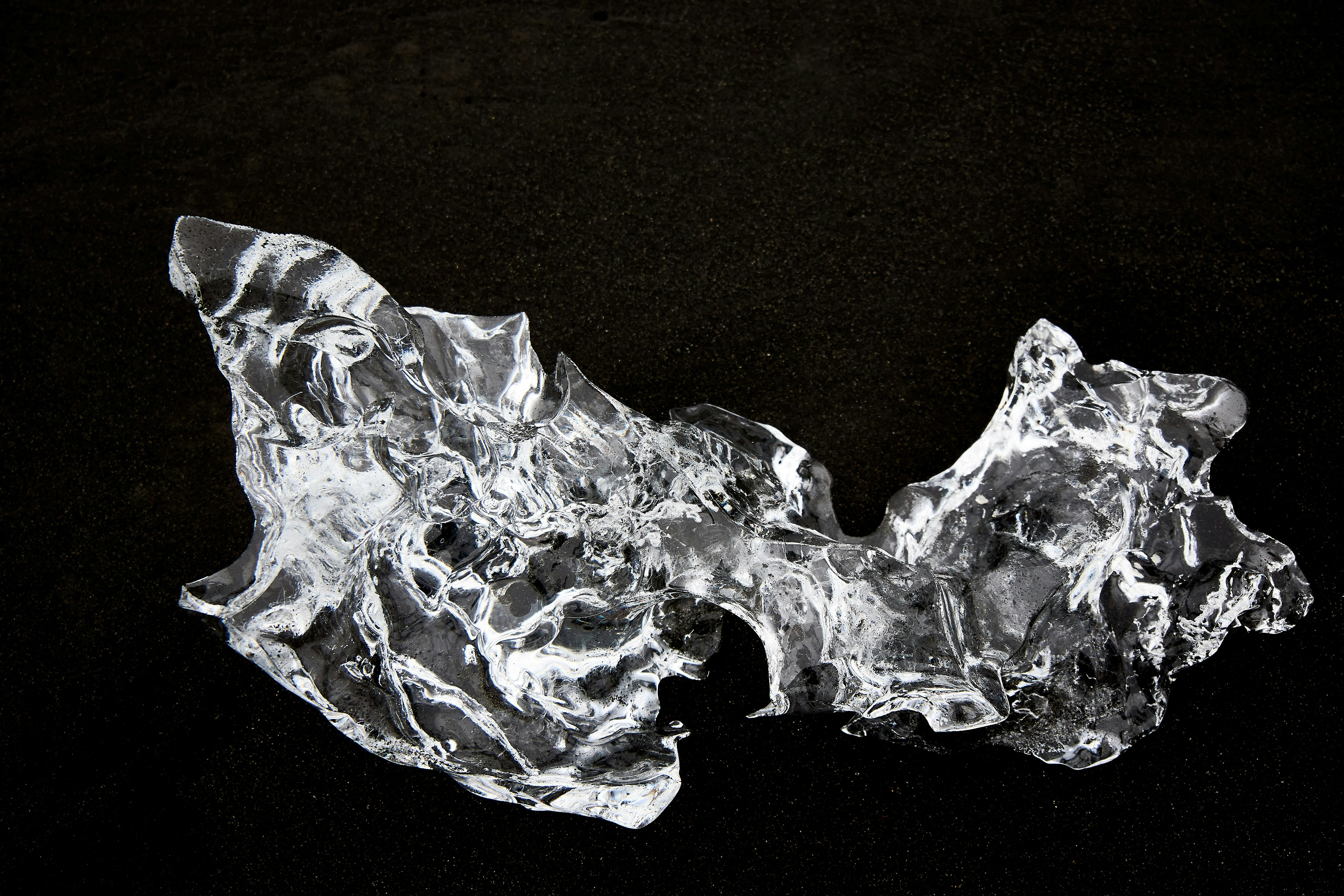 Intricate piece of ice shaped by nature, resting on a dark surface, showcasing its crystalline structure and unique formations.