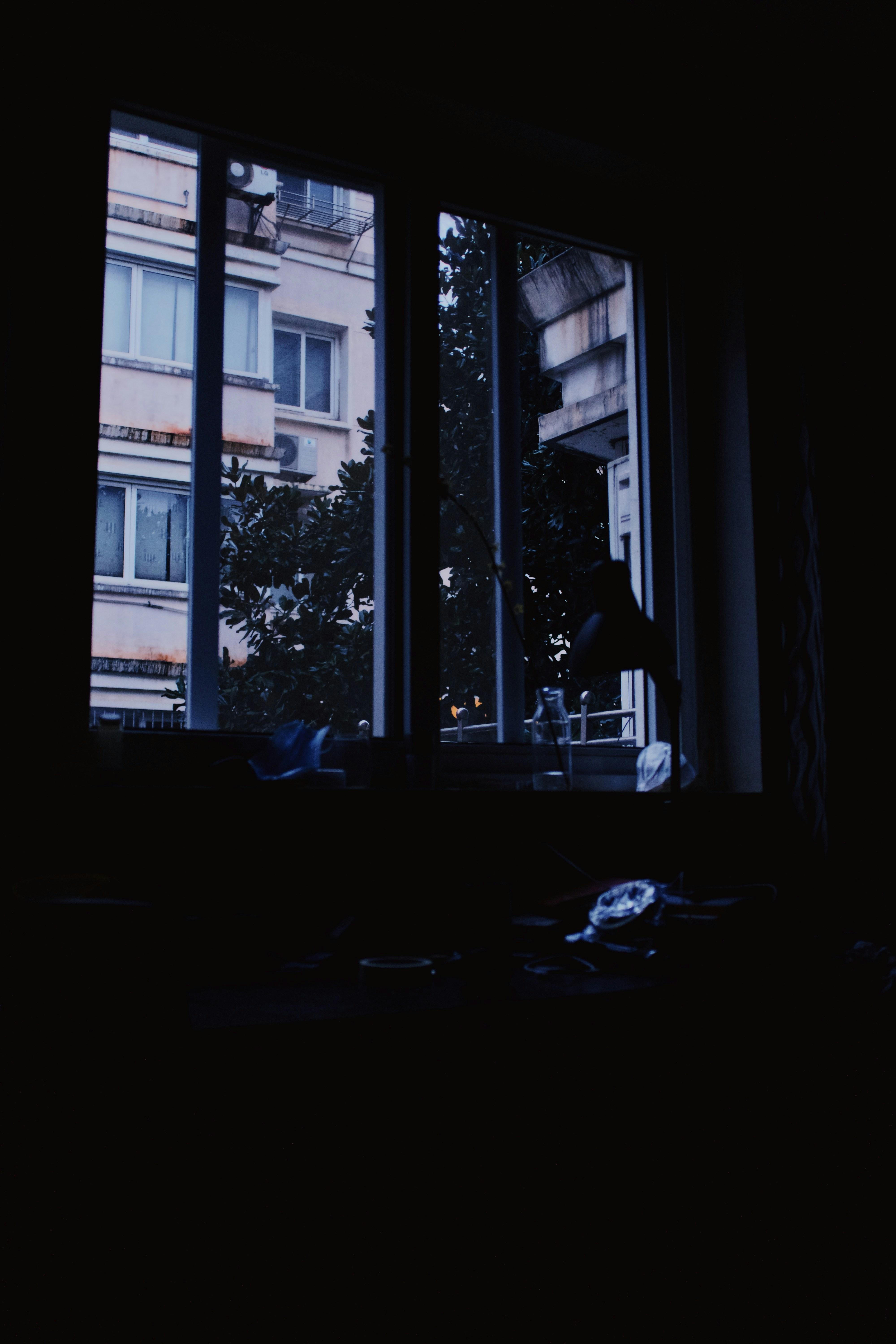 Dimly lit room with a window showcasing a view of urban architecture and greenery, capturing the essence of twilight. 