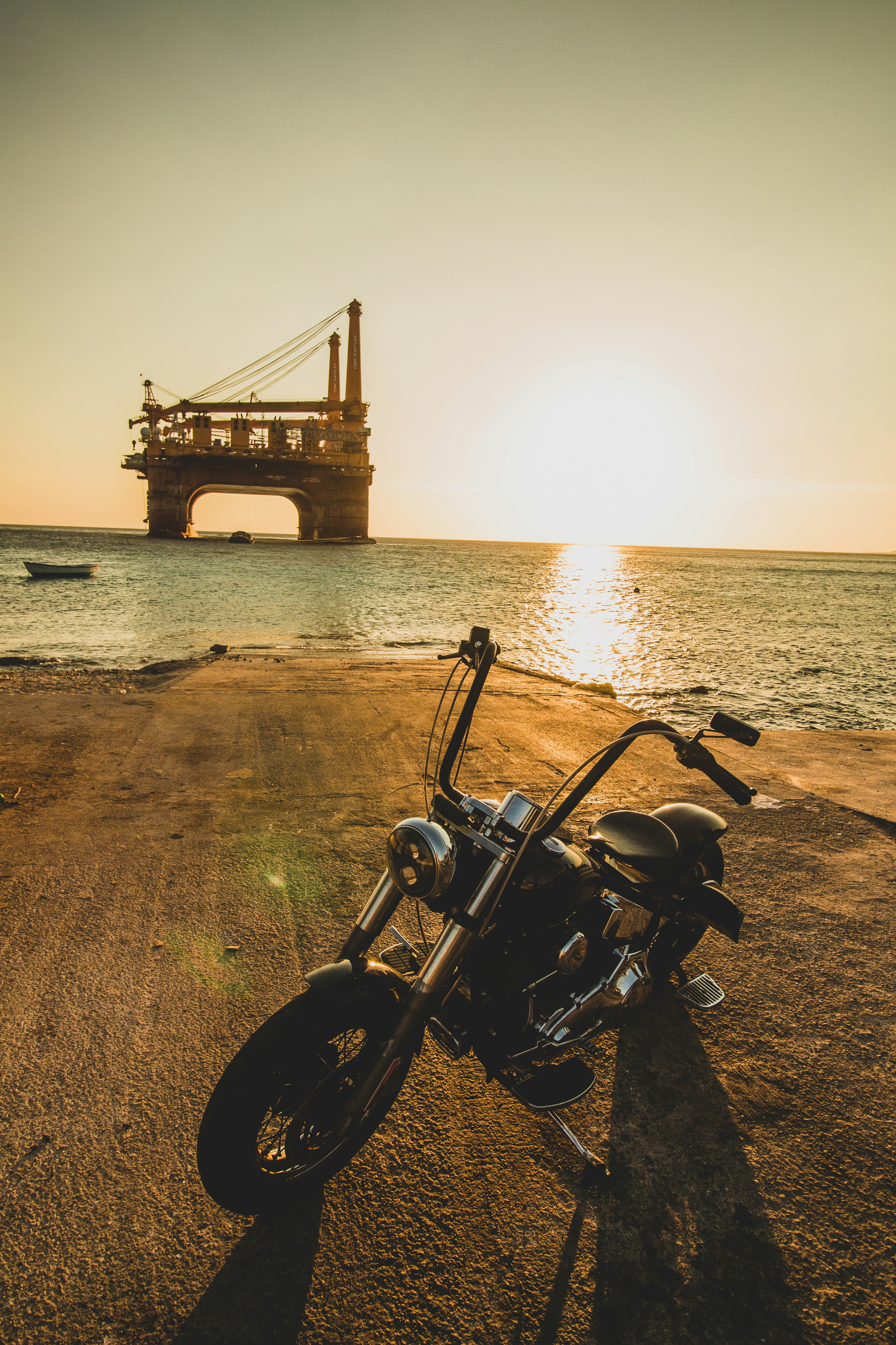 Dusk Chrome: A Motorcycle Pauses on the Pier as the Offshore Rig Silhouettes the Horizon