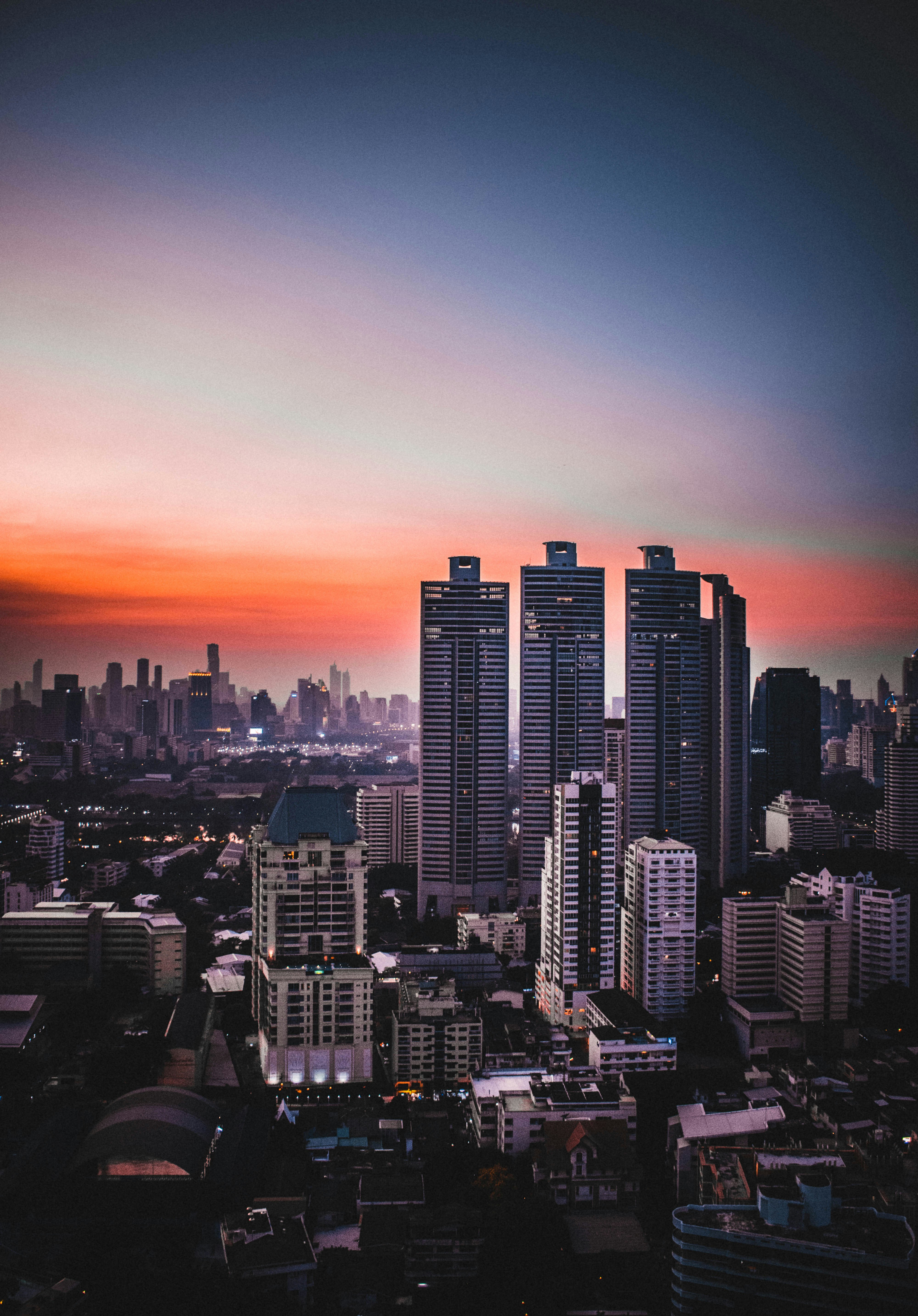 High-rise buildings silhouetted against a vibrant sunset skyline, showcasing an urban landscape transitioning into night.