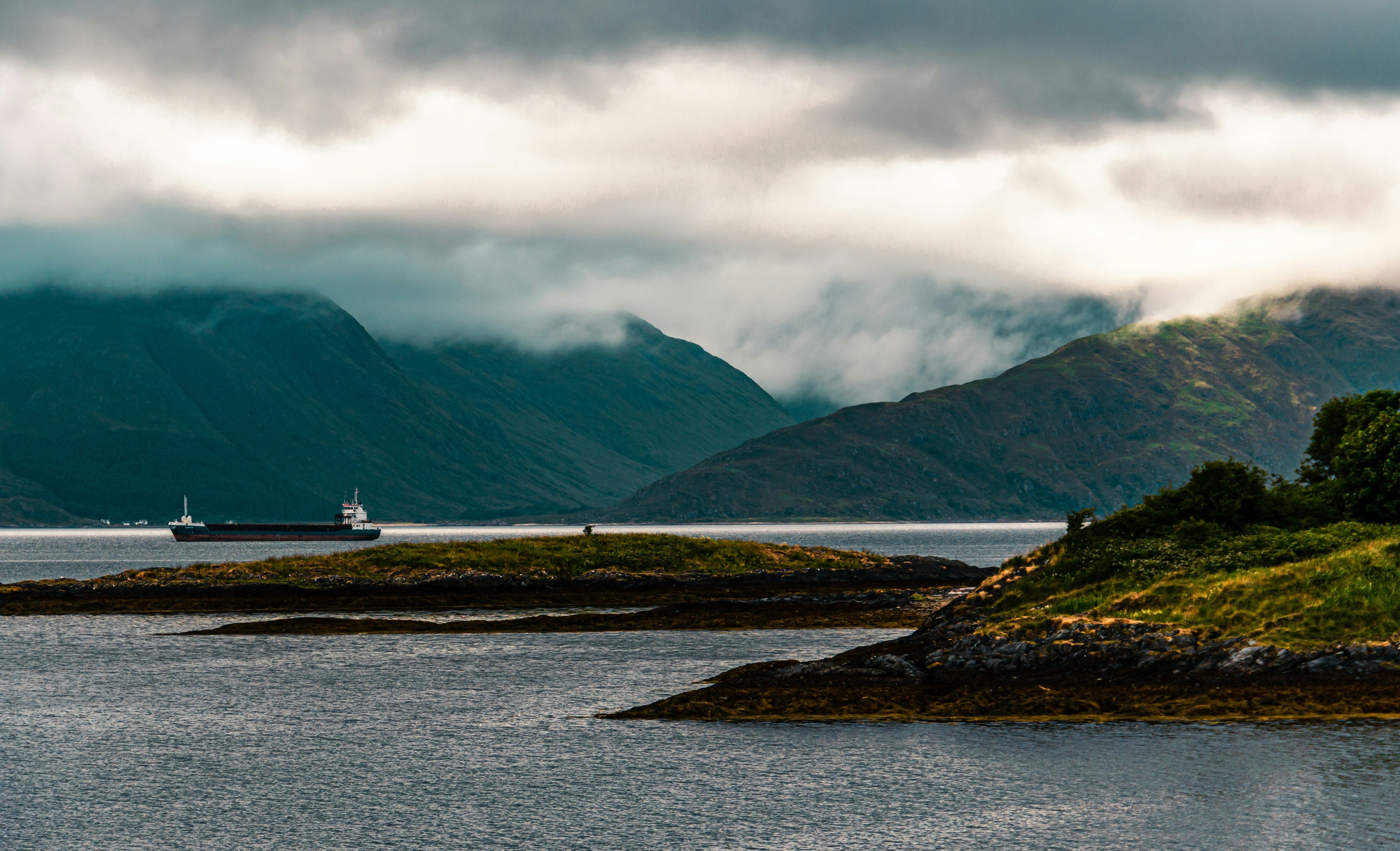 Cargo ship navigating calm waters with mist-shrouded mountains in the background.