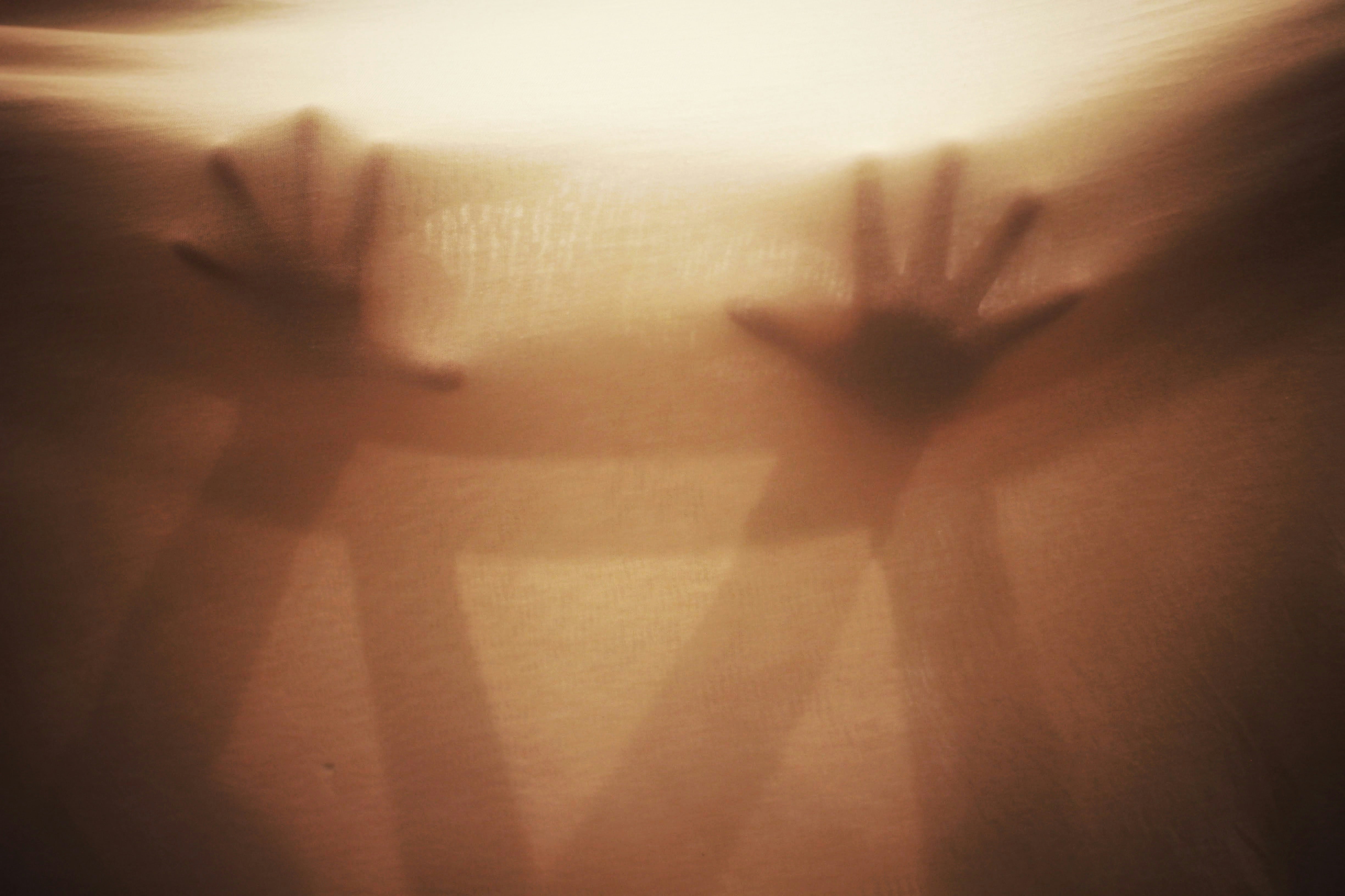 Shadowy hands pressed against a softly lit fabric surface.