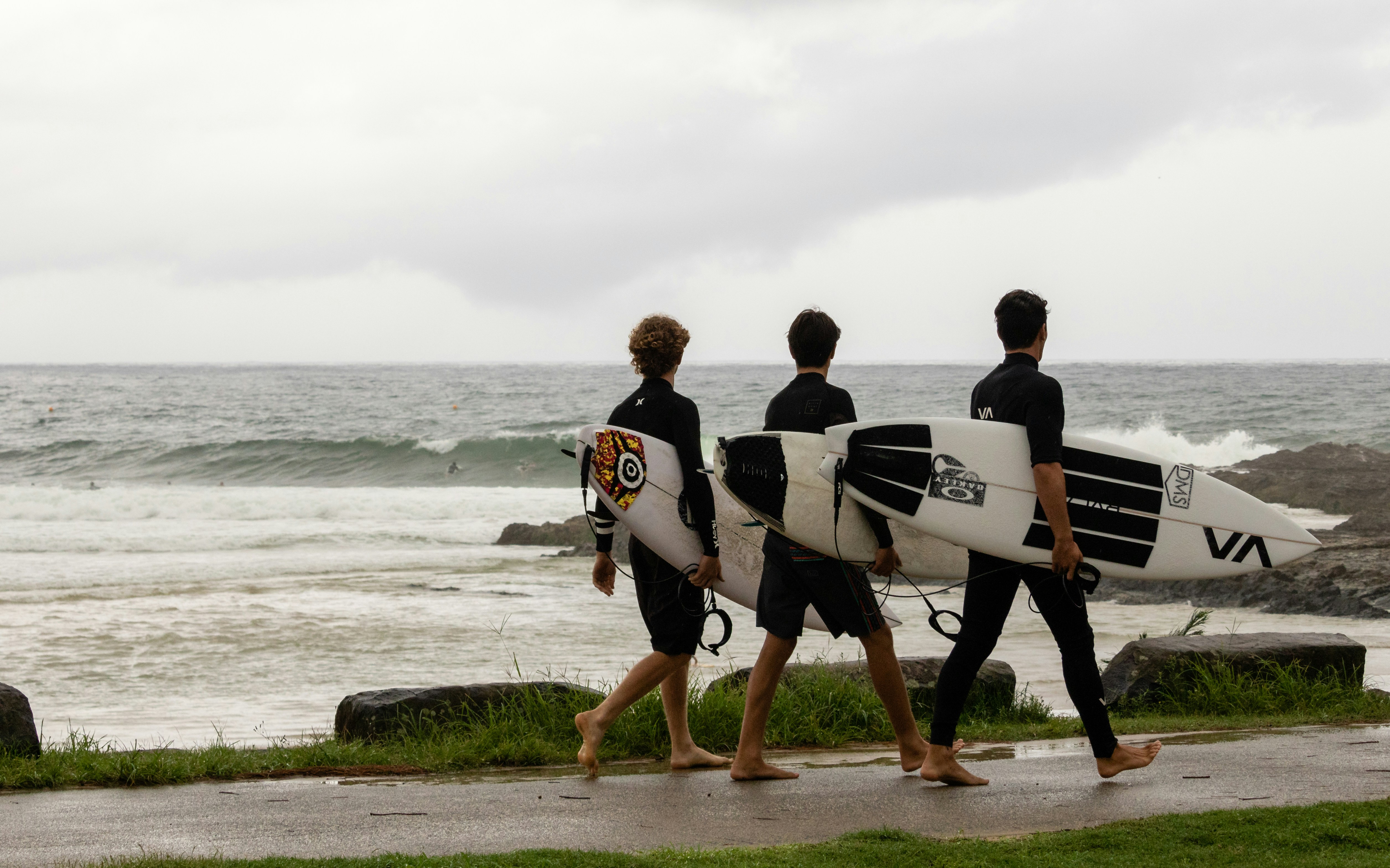 Three Surfers Walk the Shore with Boards Thawing the Morning Sea