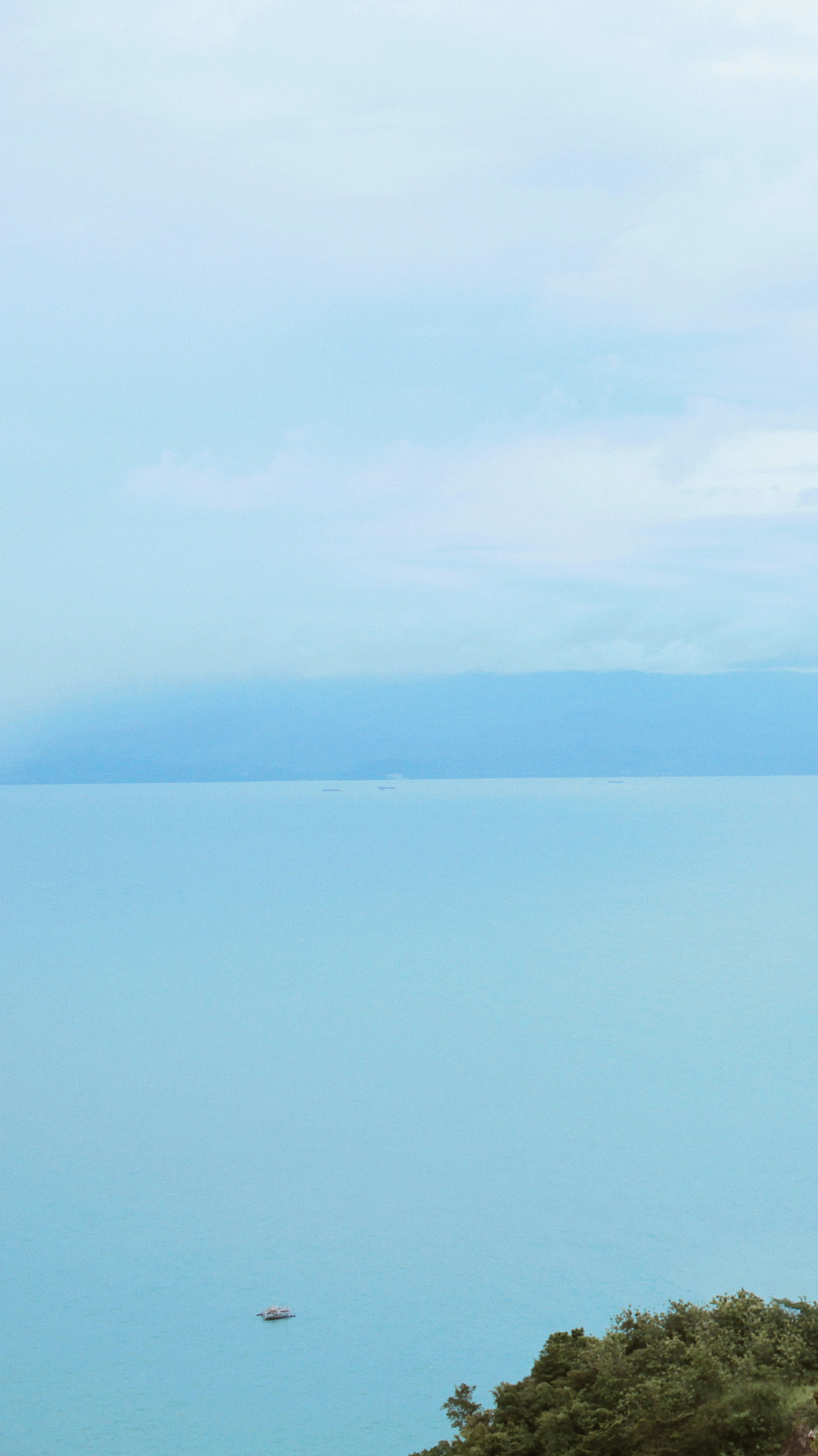 Expansive view of a calm blue sea meeting a cloudy sky with distant mountains.