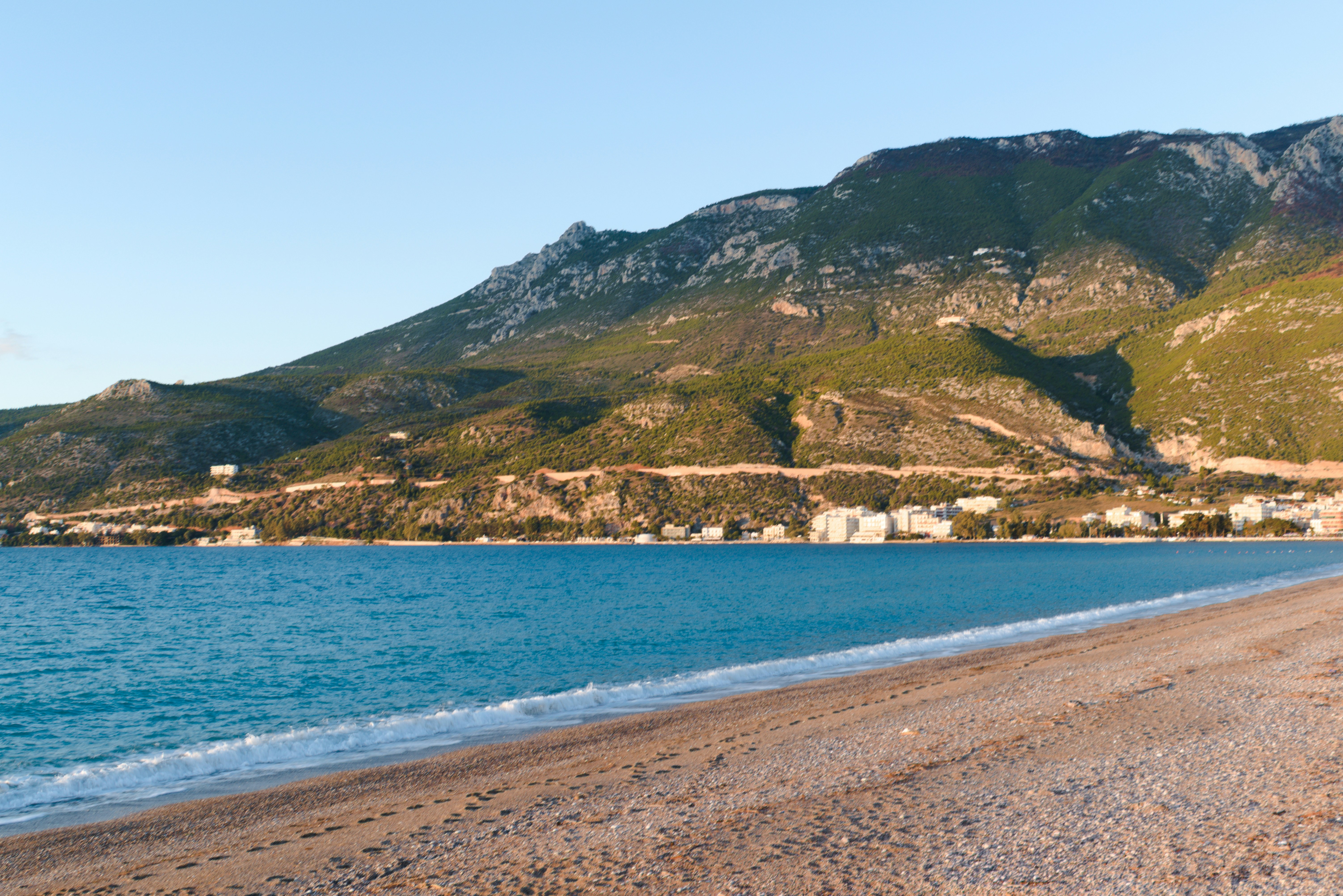 Expansive mountain range meets a tranquil sea under a clear blue sky.