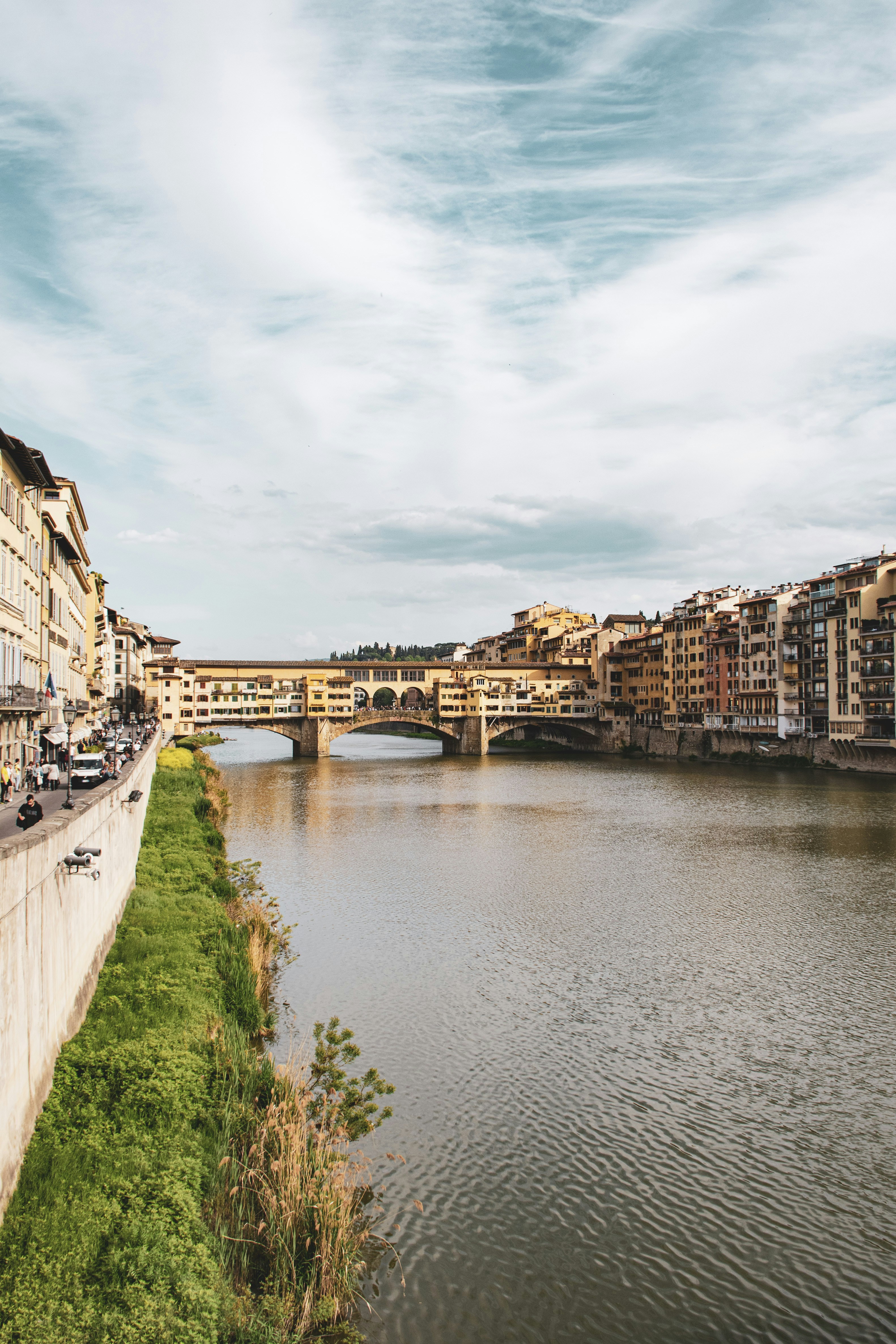 The iconic Ponte Vecchio spans the Arno River, flanked by historic buildings and lush greenery along the banks.