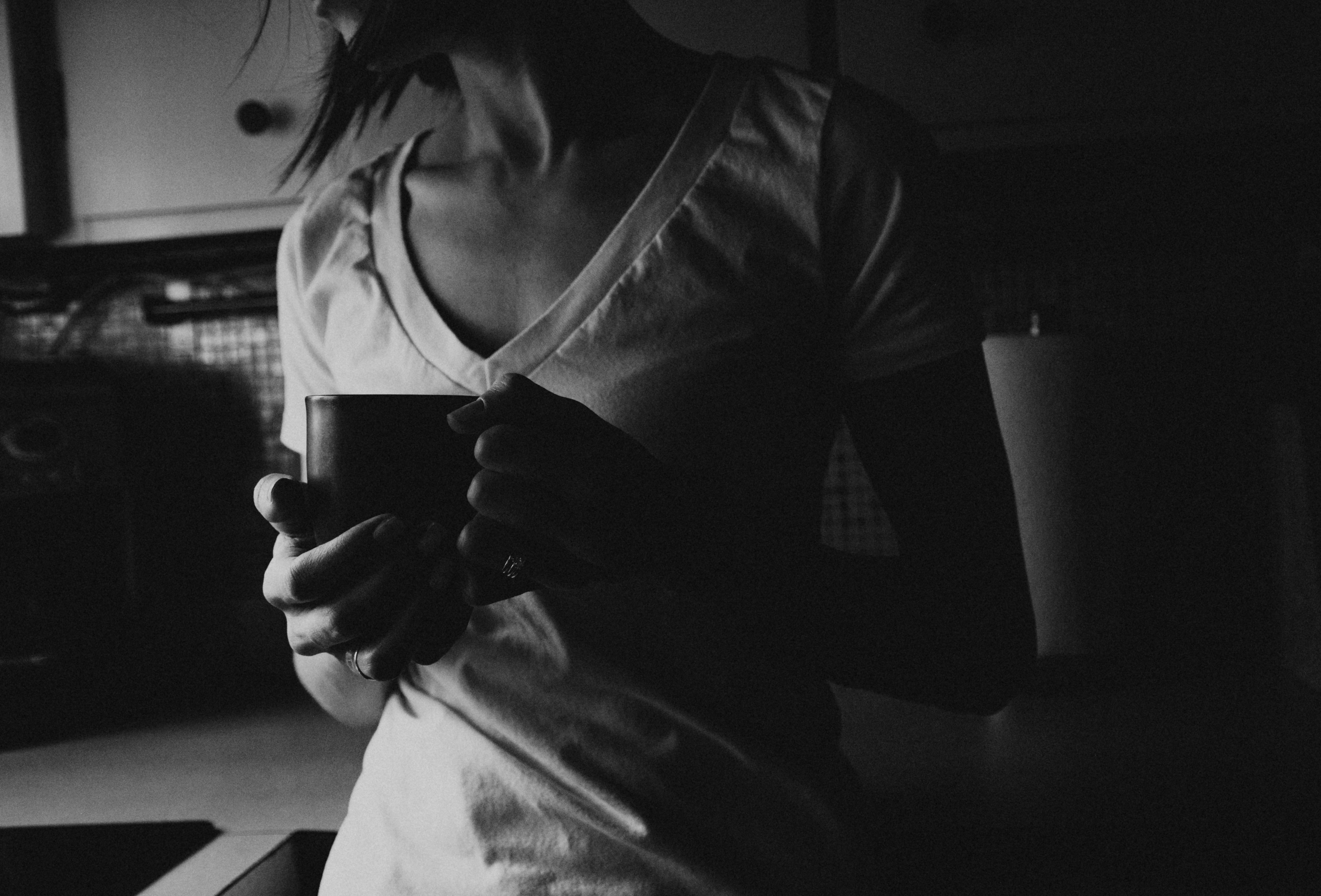 Shadowed Hands Cradle a Mug in a Dim Kitchen