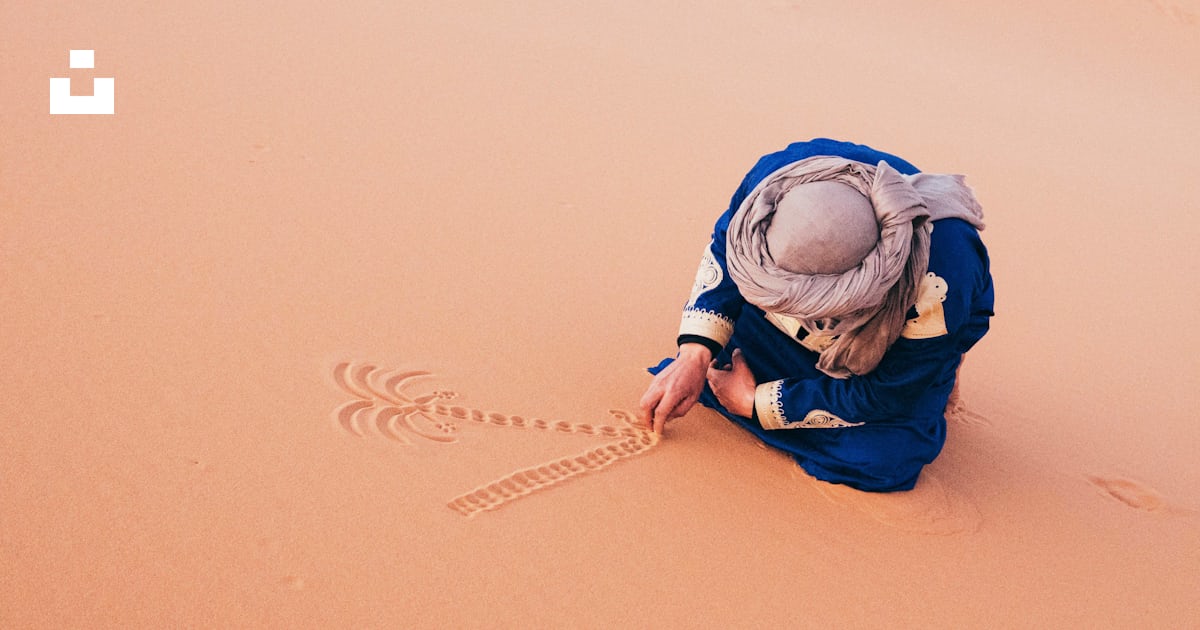 Man In Blue Jacket And Blue Denim Jeans Sitting On Brown Sand During