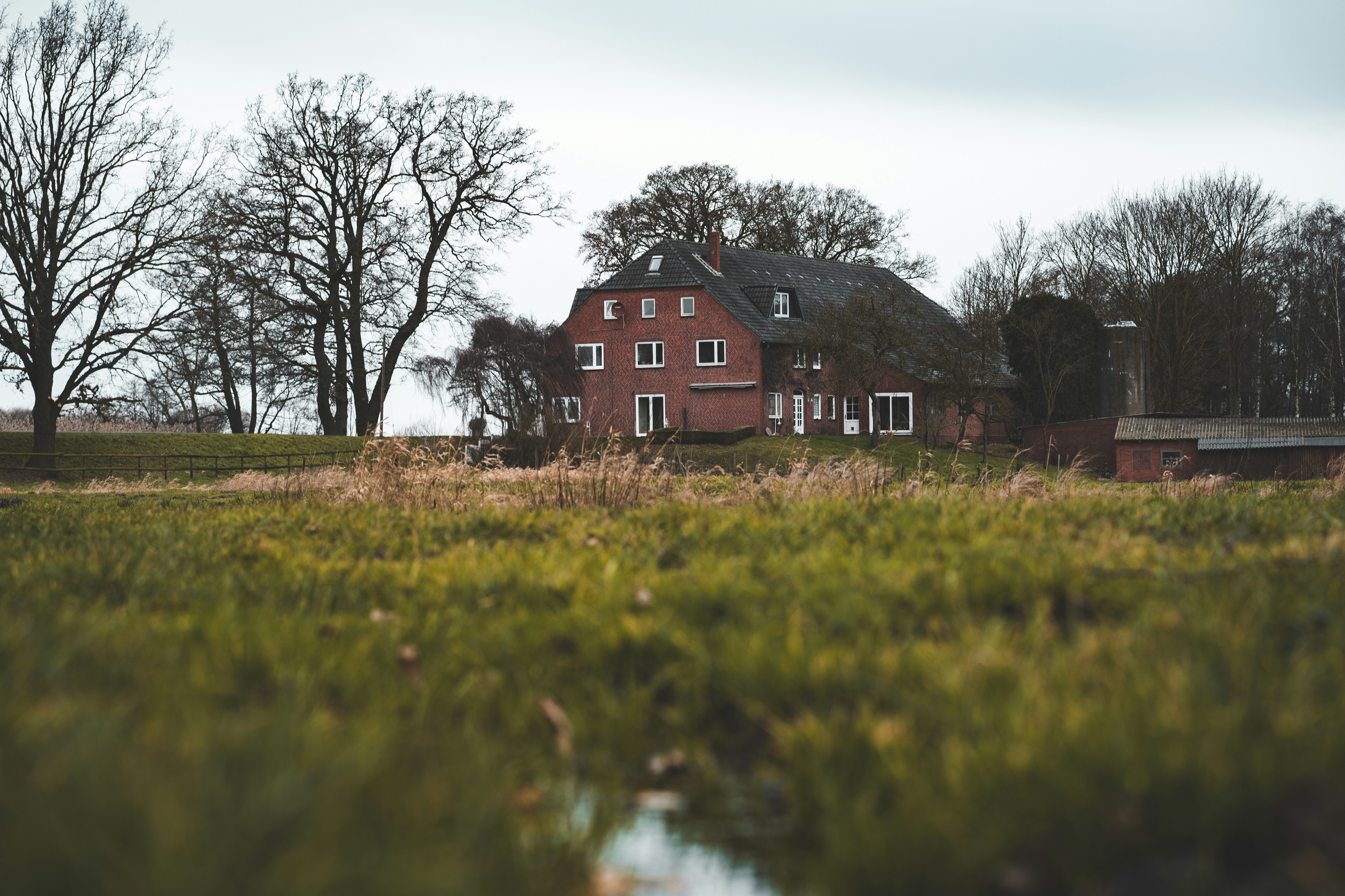 Brown and white house surrounded by bare trees under a cloudy sky.