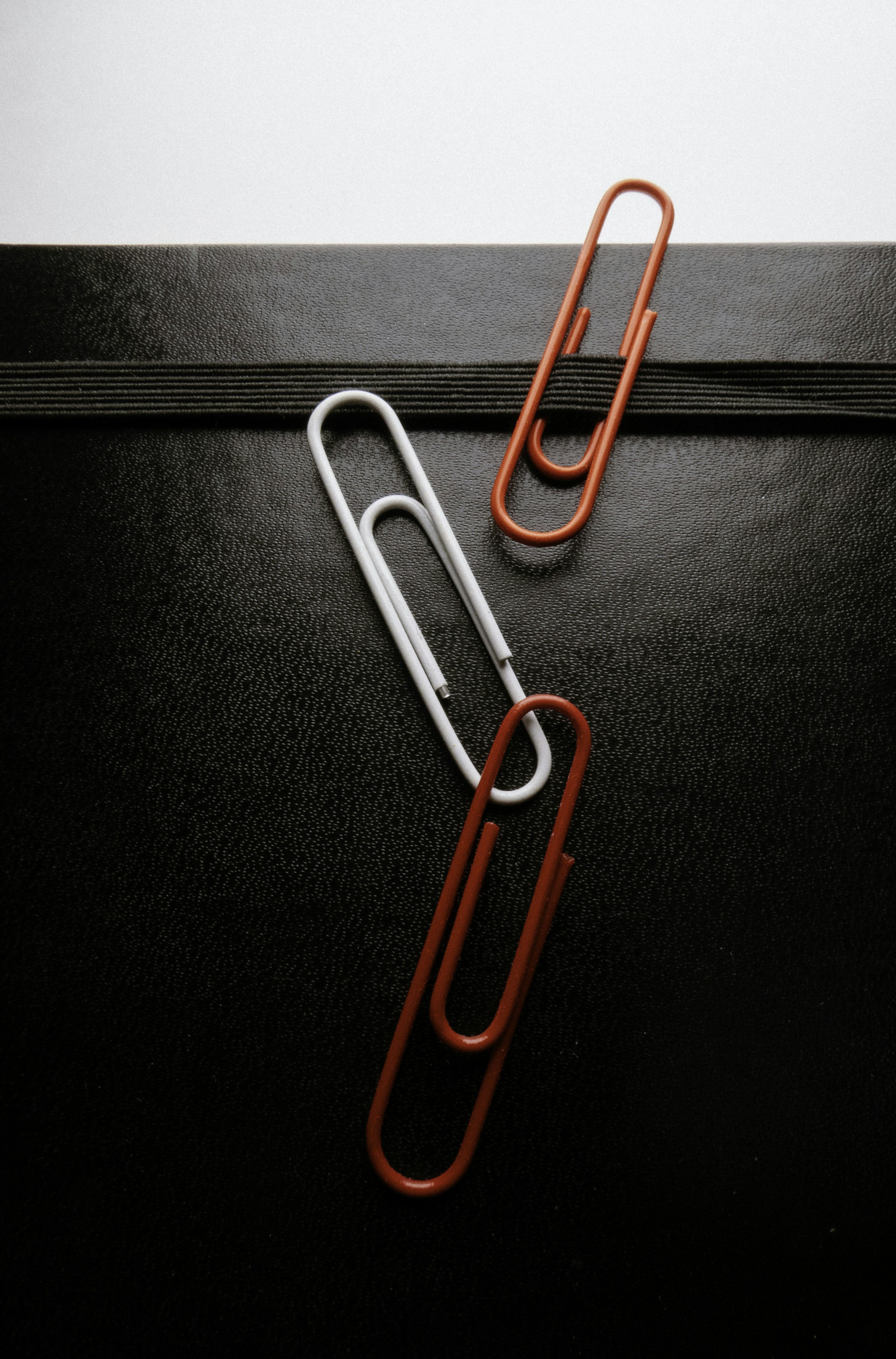 Red and white paper clips rest on a textured black notebook.