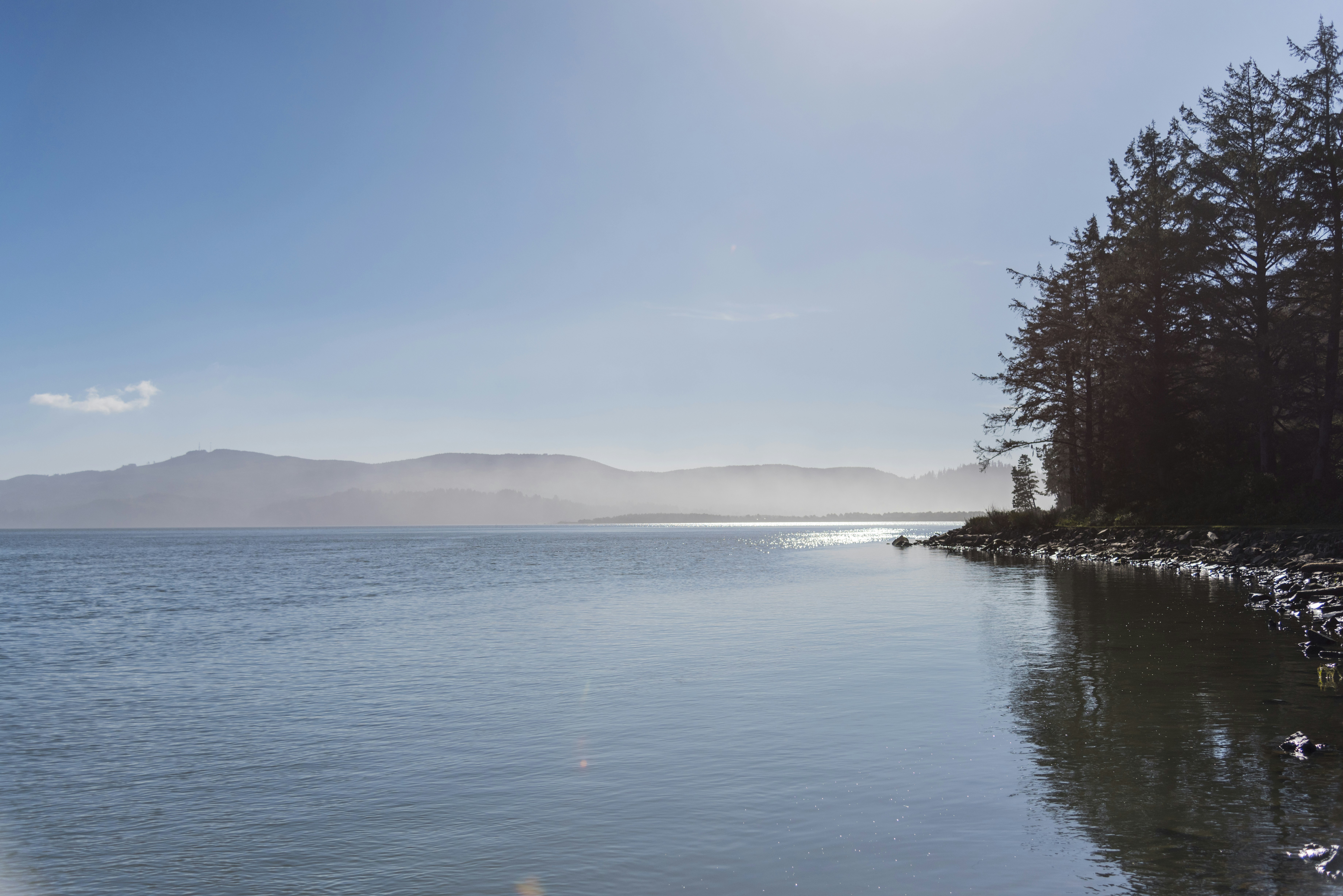 Serene coastline with misty hills in the background and shimmering water reflecting the morning light.