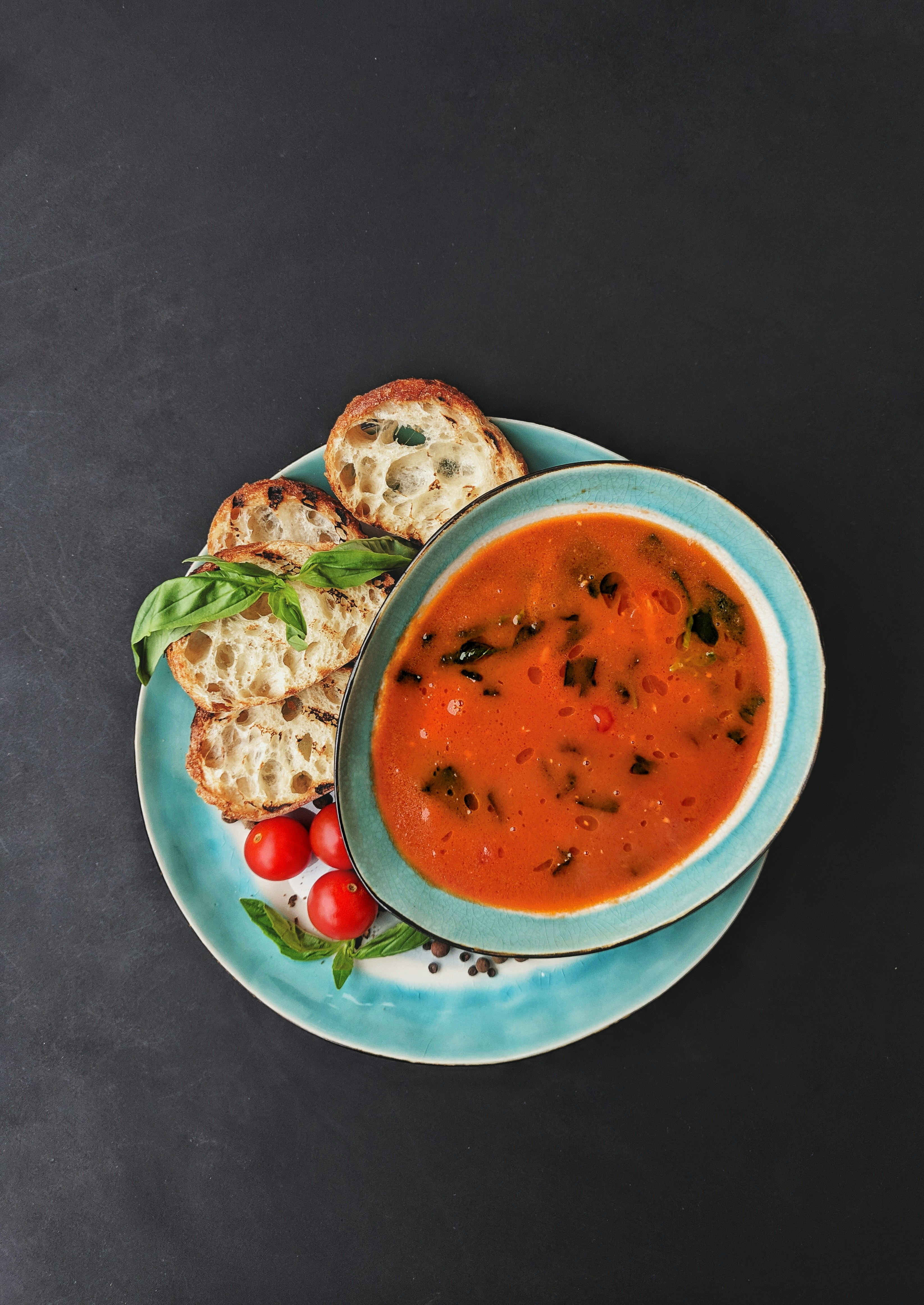 Vibrant Tomato Soup on a Teal Plate with Rustic Breads