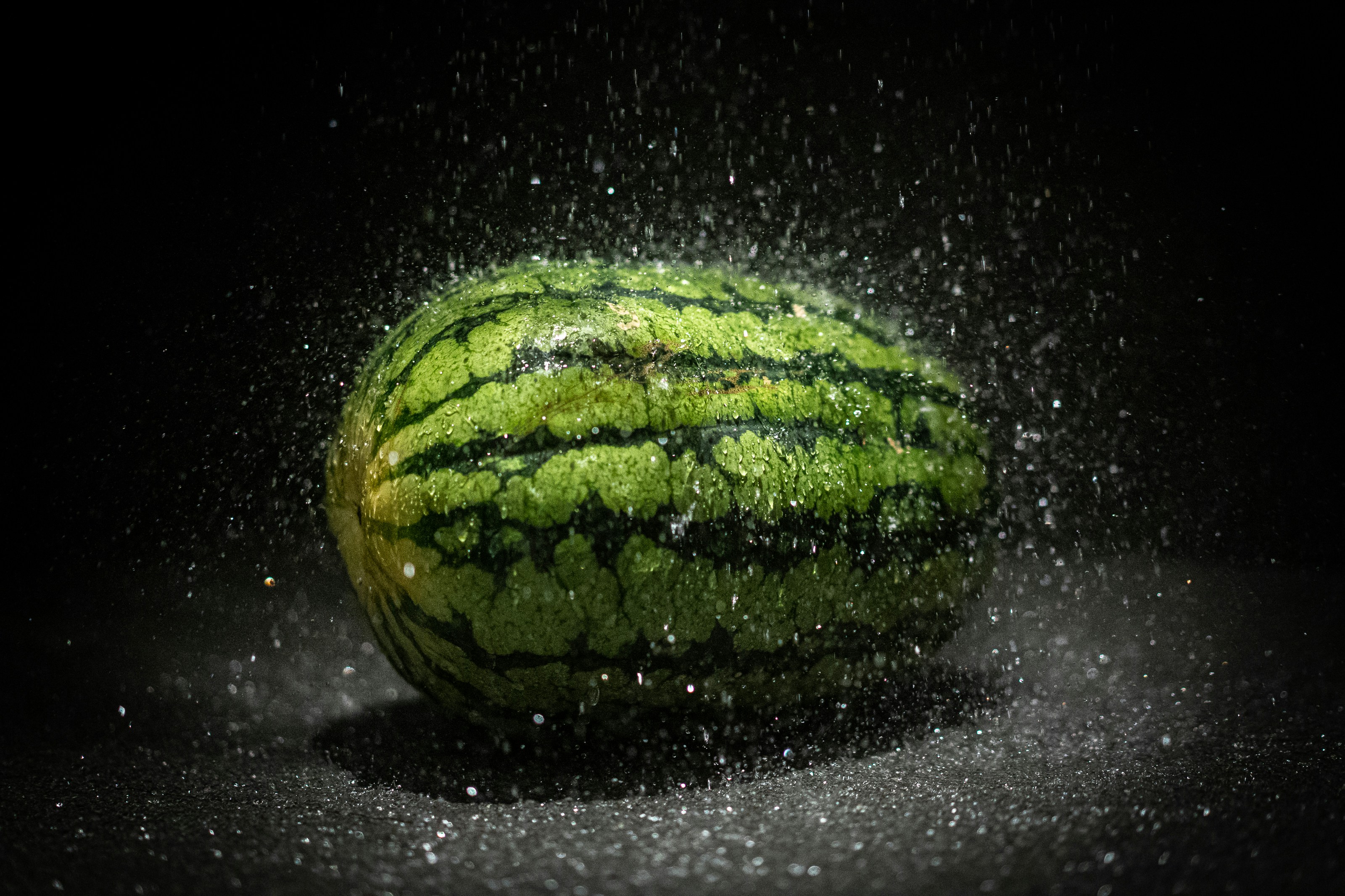 Watermelon taking a shower on a dark background with droplets splashing