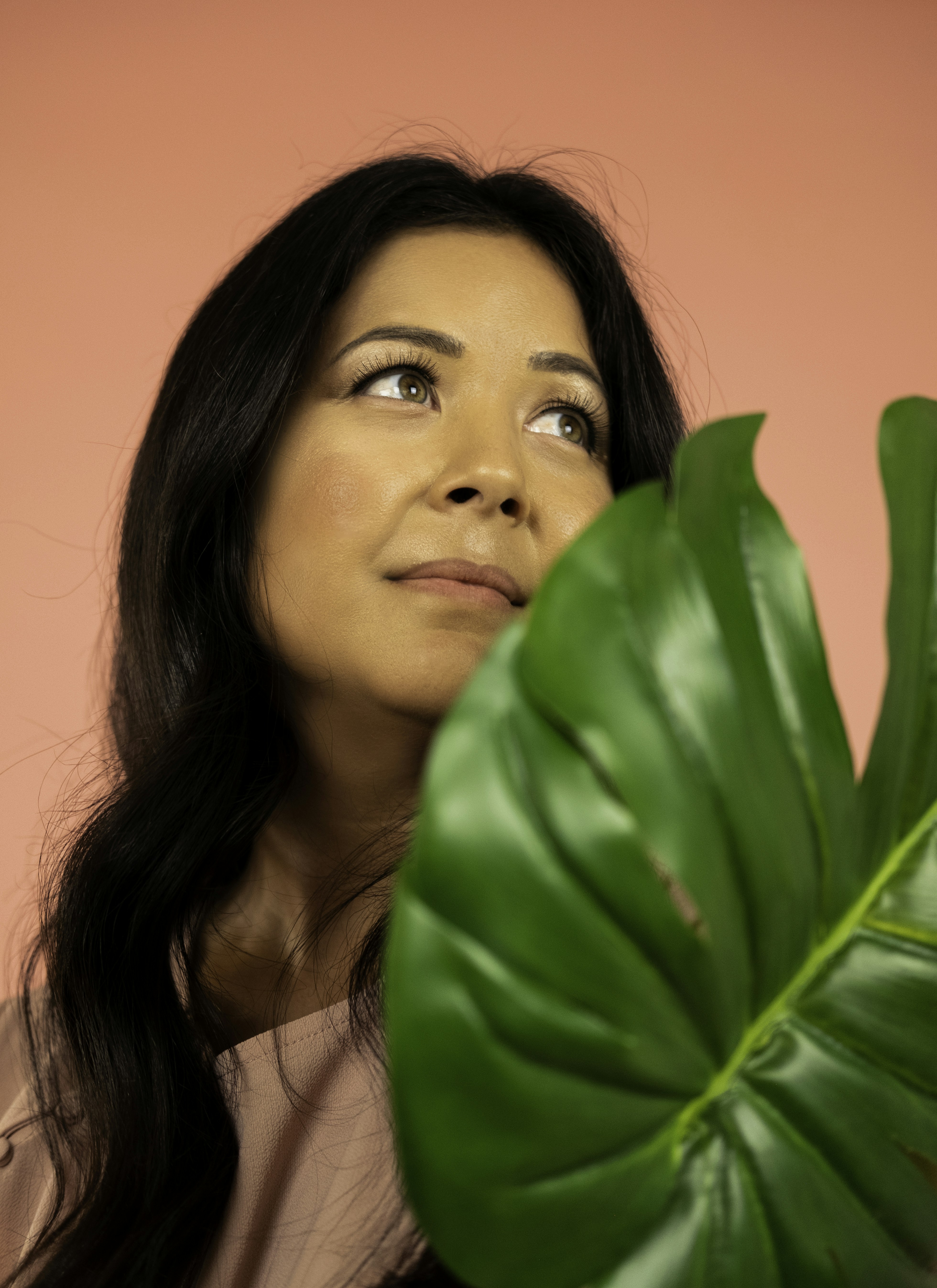 Gaze Through a Tropical Veil: Portrait Framed by a Leaf on a Coral Backdrop