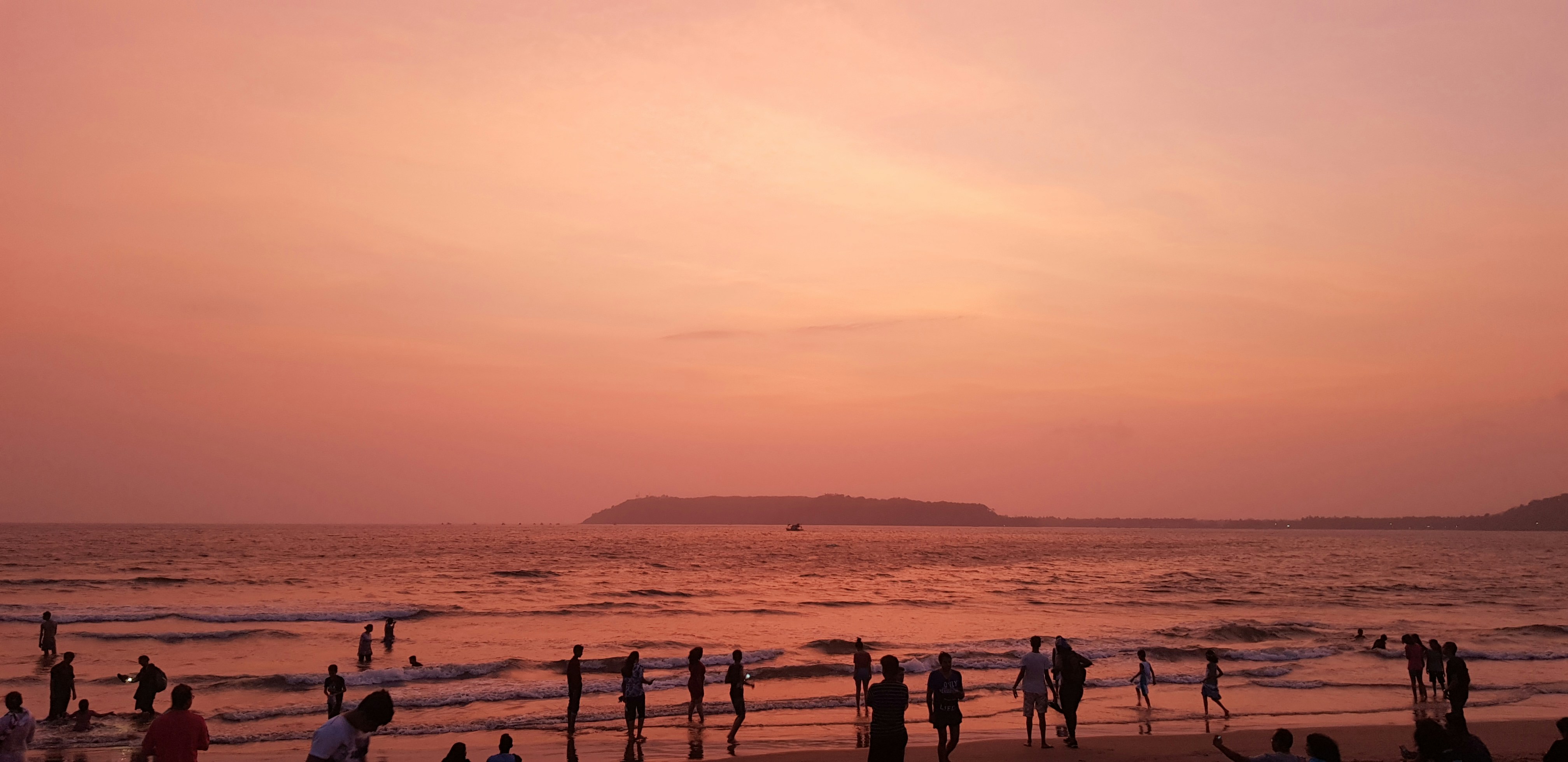Silhouetted figures enjoying a serene beach under a warm, pink sunset sky.