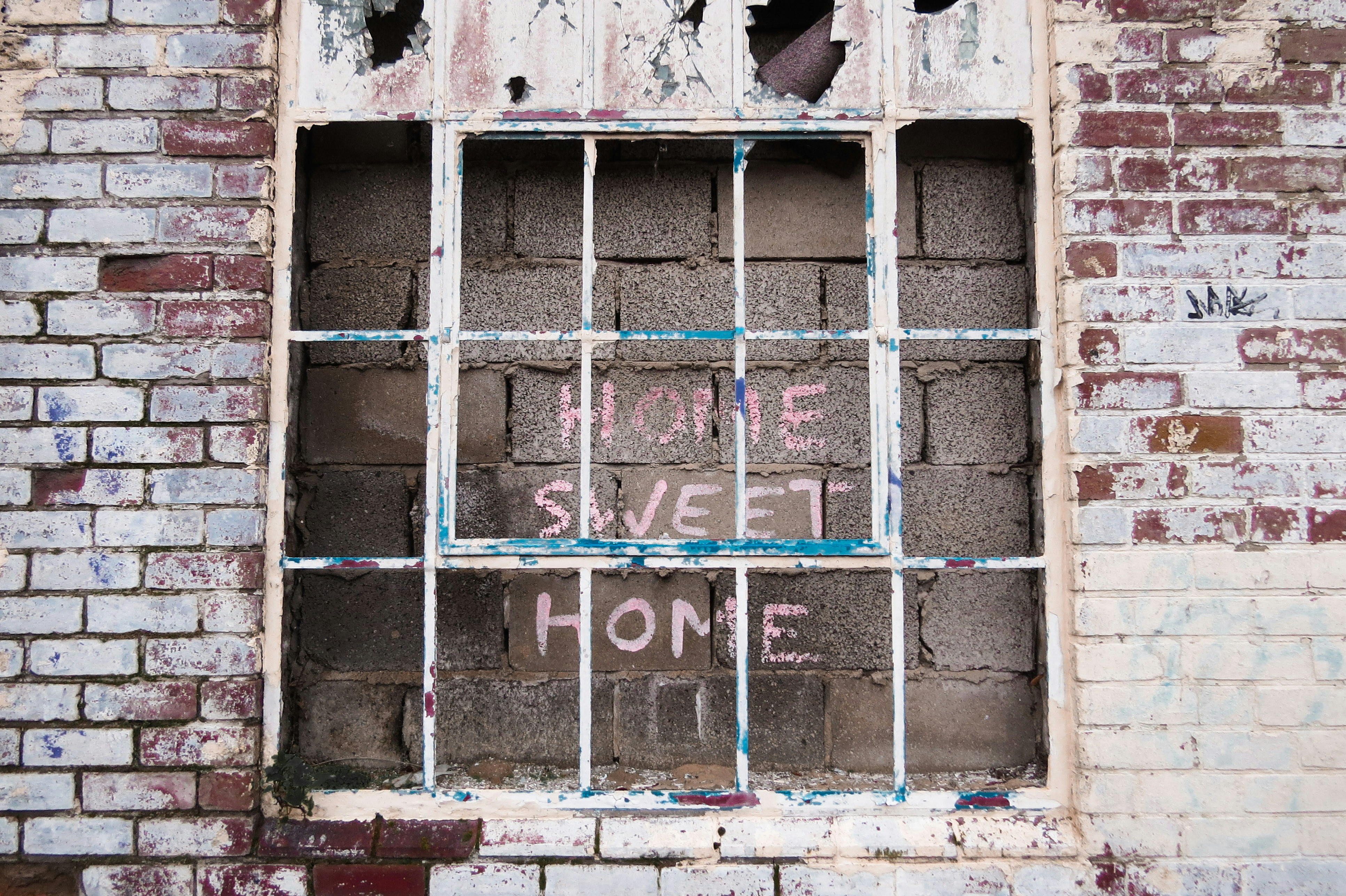 Chalked message 'HOME SWEET HOME' visible behind a metal-barred window set in a weathered brick wall.